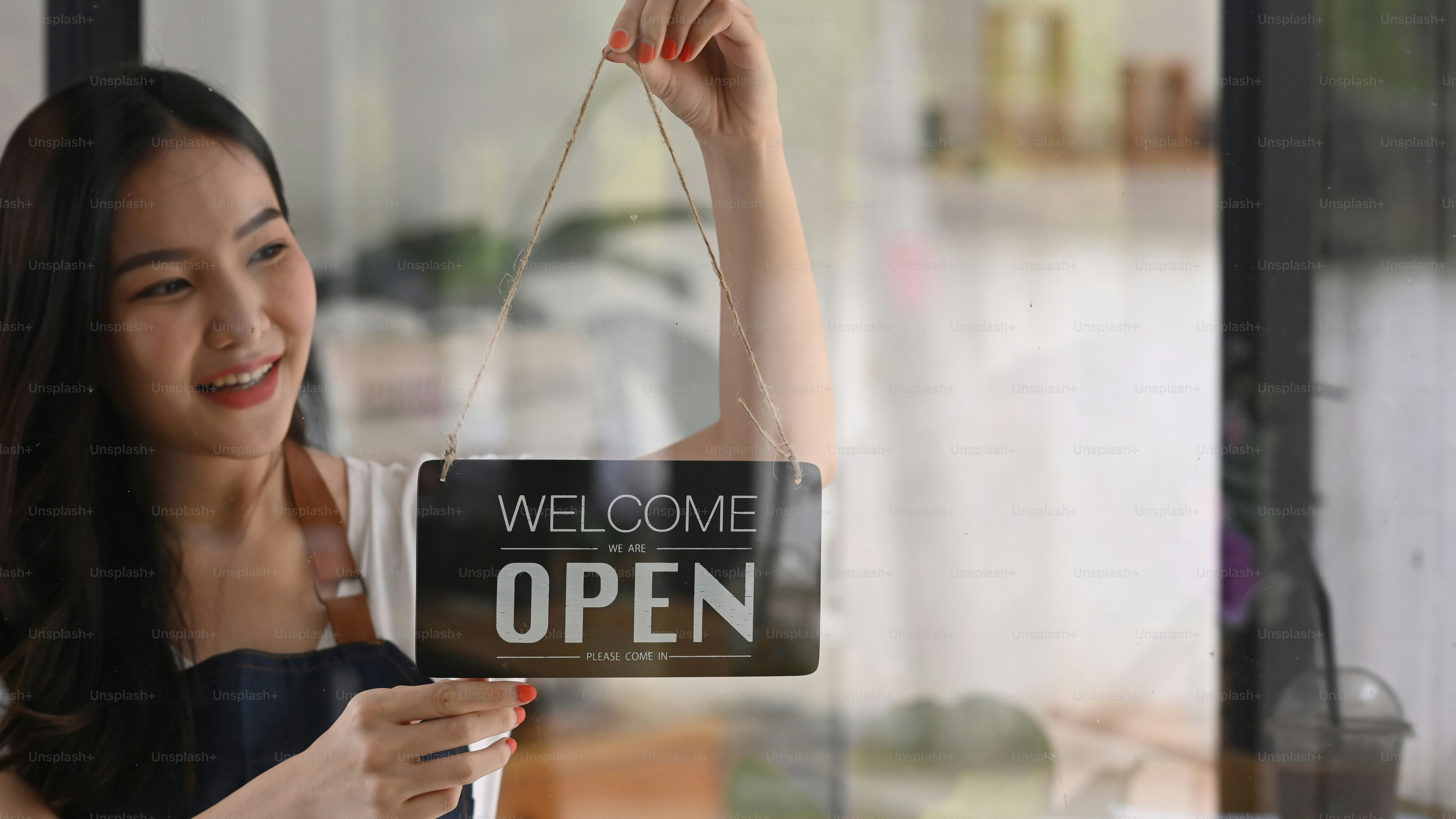 Smiling woman owner turning open sign board on glass door in modern ...