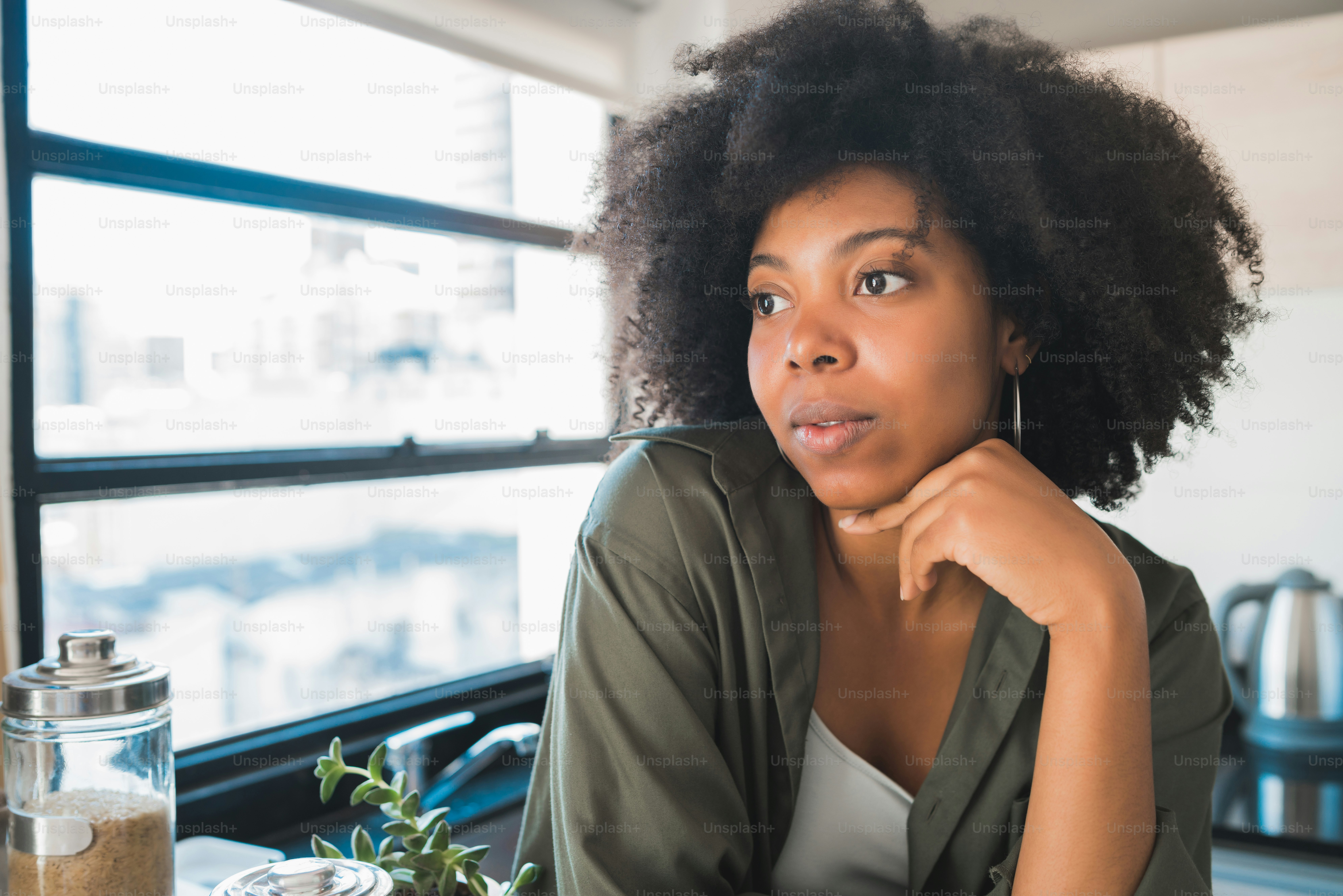 Portrait of young afro woman relaxing and looking pensative at home ...