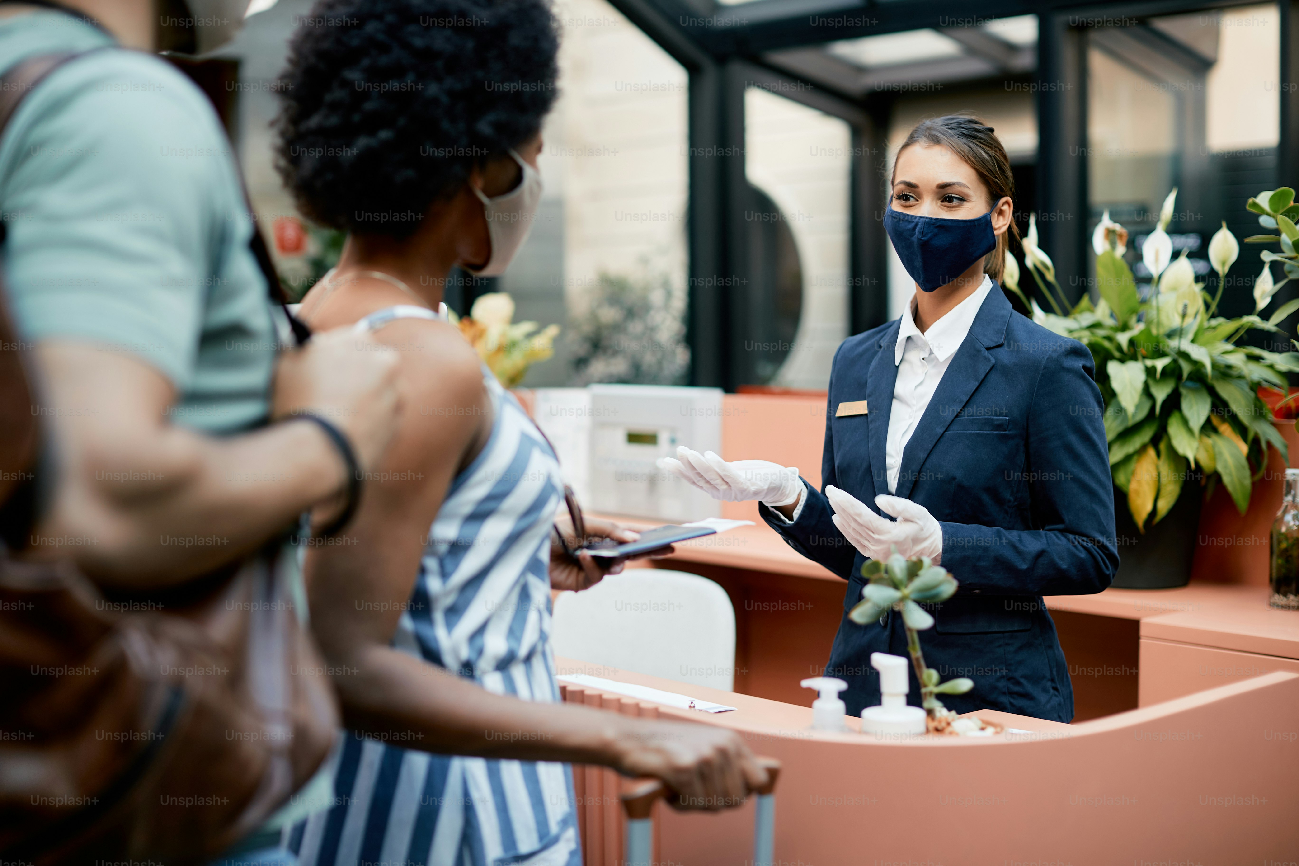 Happy hotel receptionist wearing protective face mask while ...