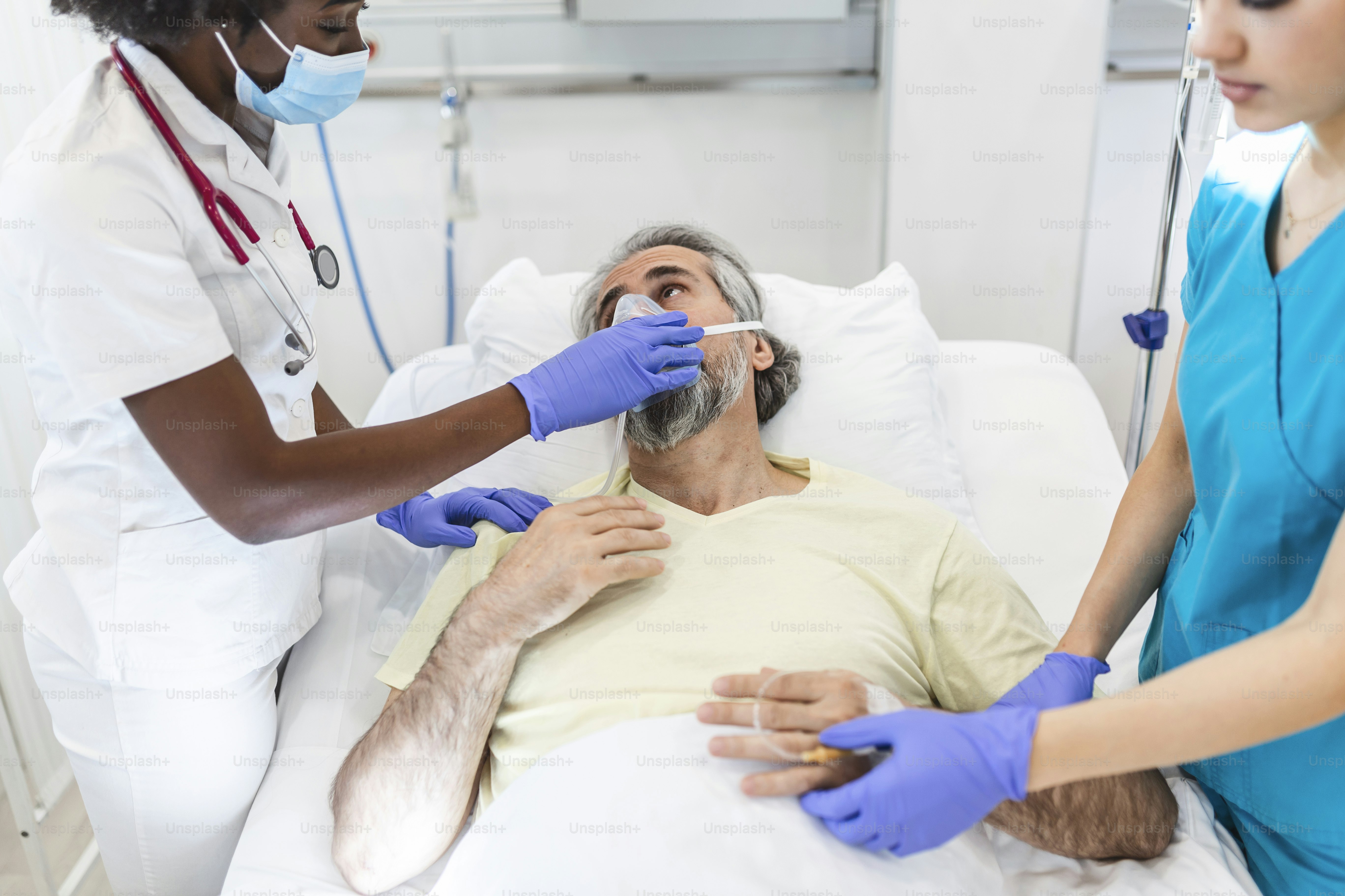 Female doctor talking with patient along coworker in ICU. Man is lying ...