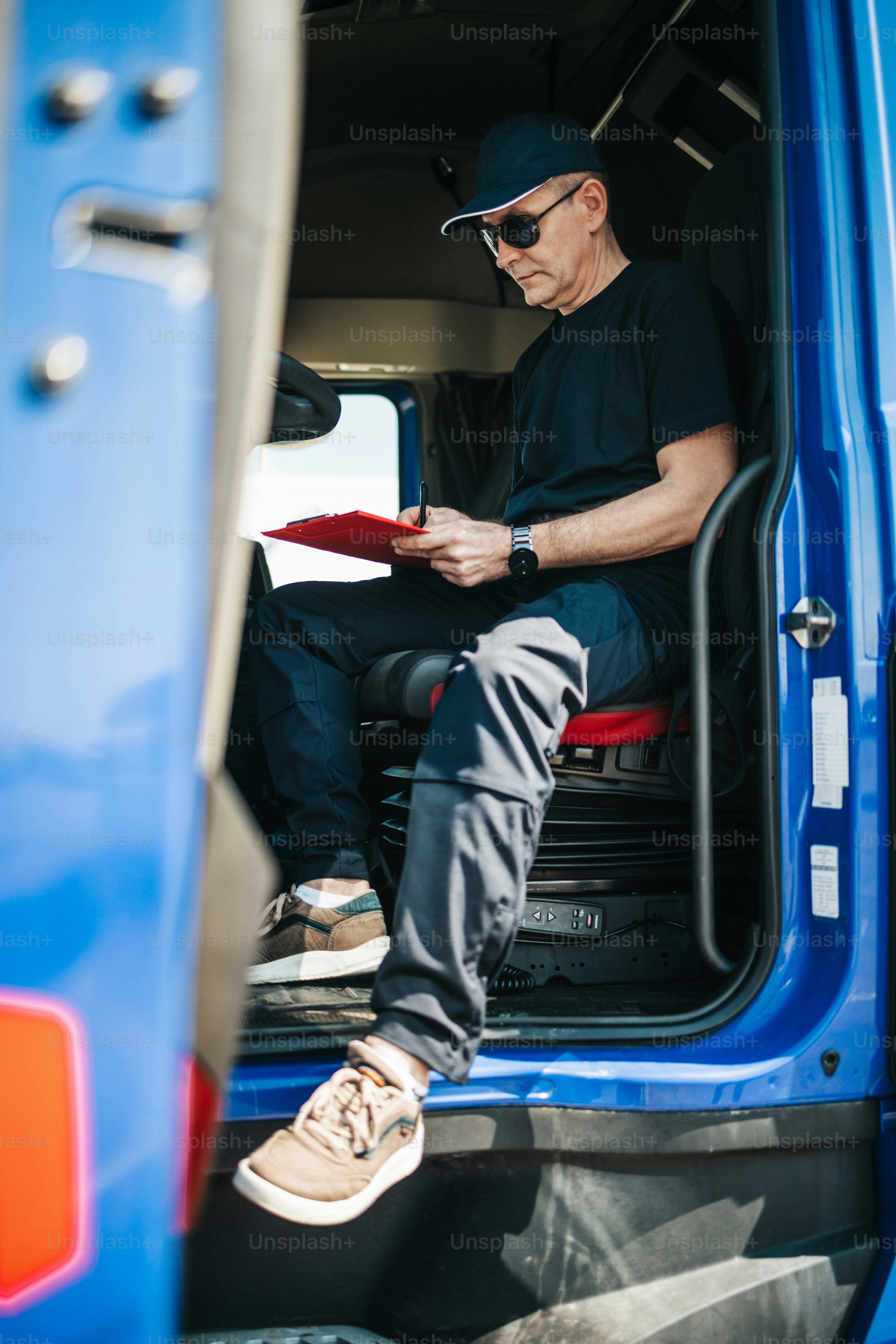 Handsome experienced male truck driver with a hat sitting and driving ...