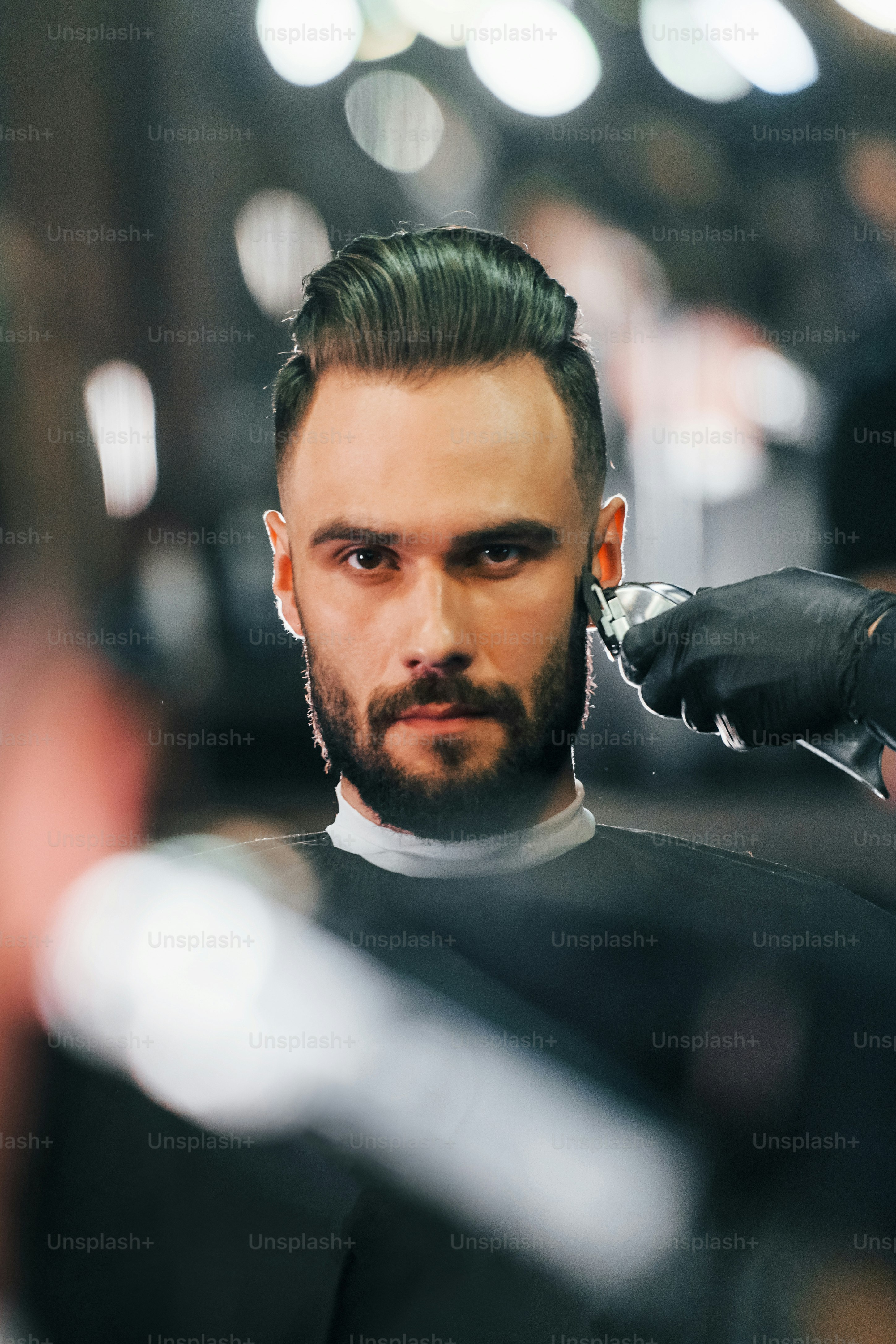 Young man with stylish hairstyle sitting and getting his beard shaved ...