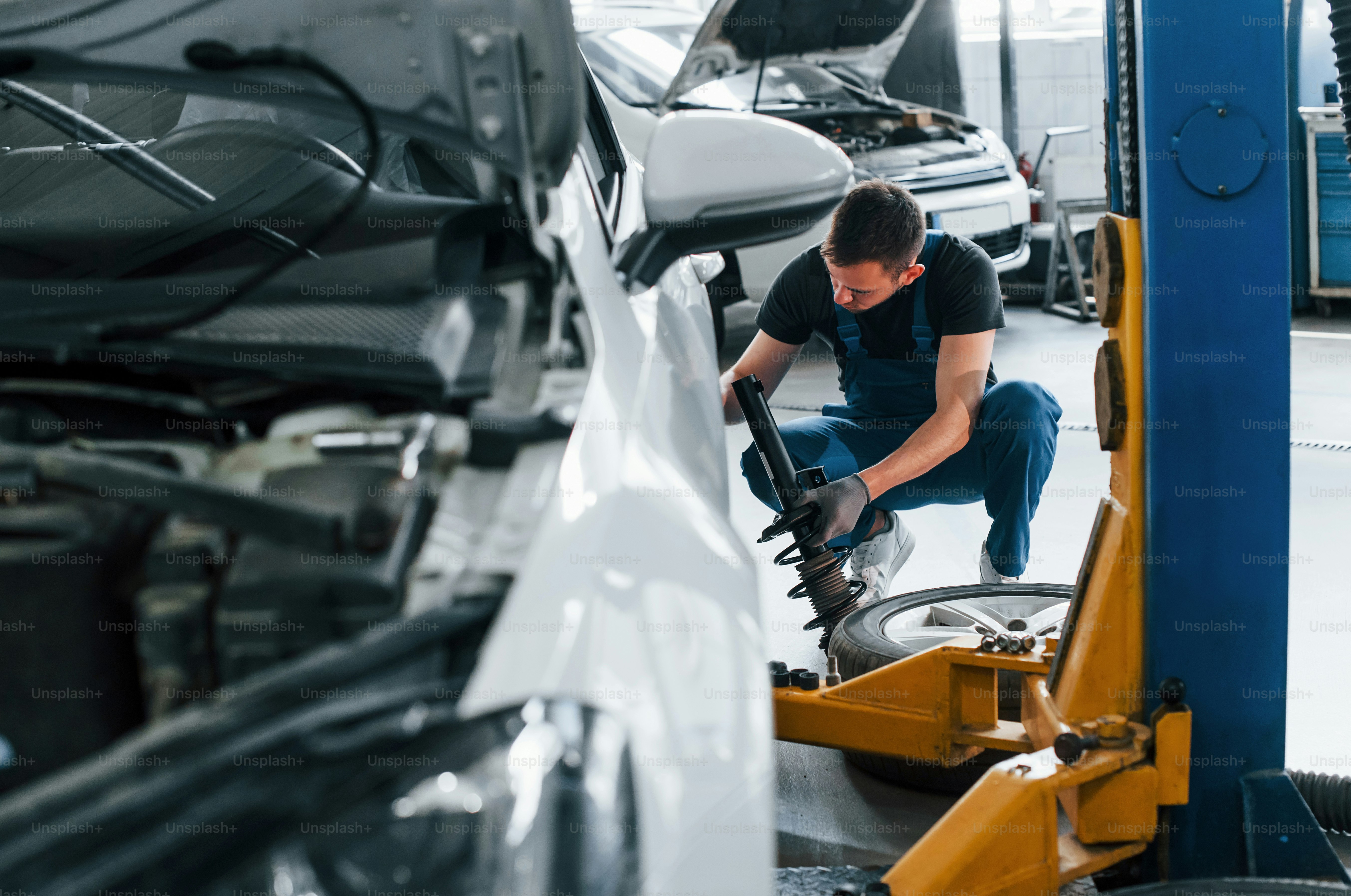 Man in work uniform repairs car indoors. Conception of automobile ...