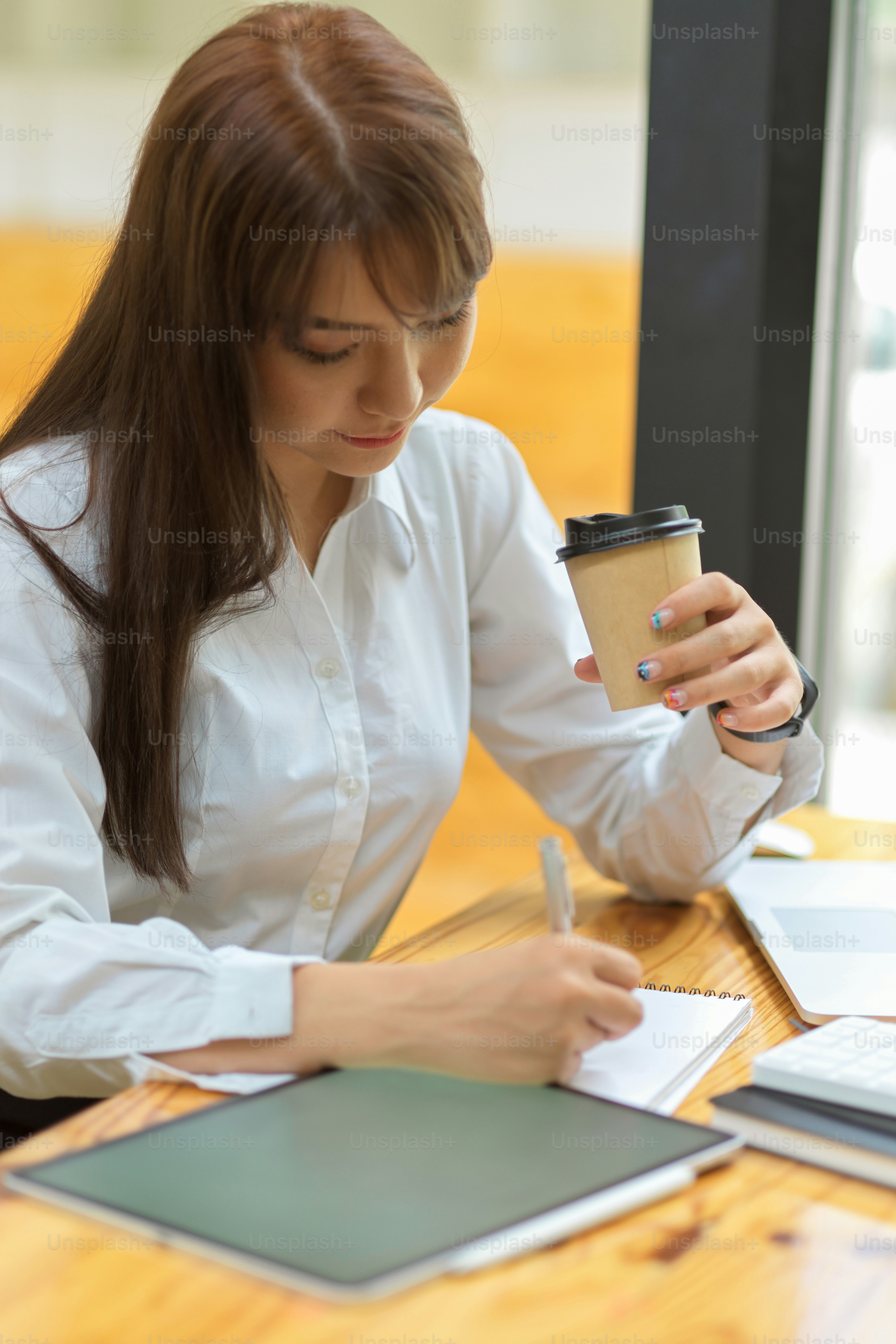 Serious focused secretary working on tablet and drinking coffee at workplace, female student ...