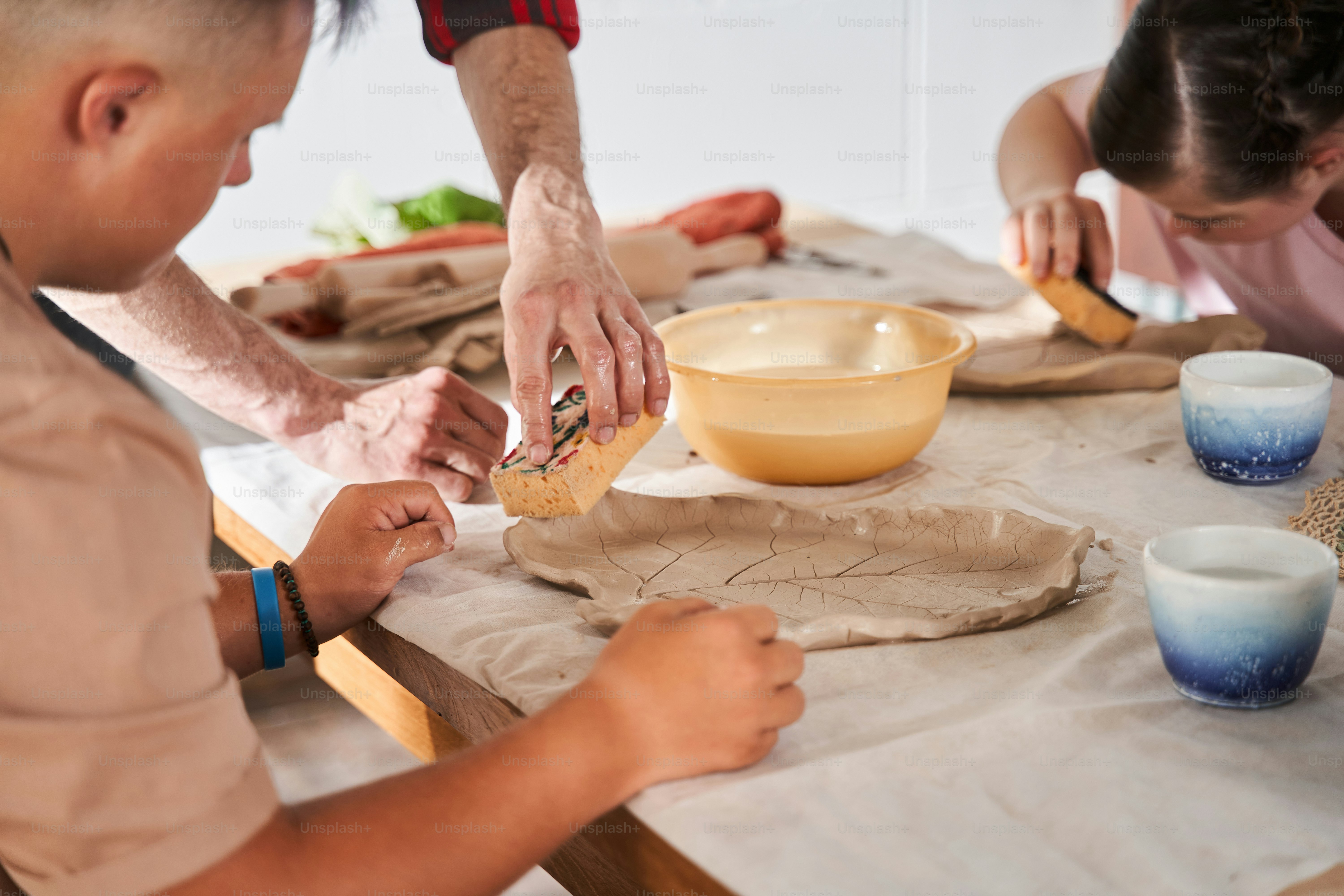 Wet the edges. Cropped view of the sculptor holding sponge and touching ...