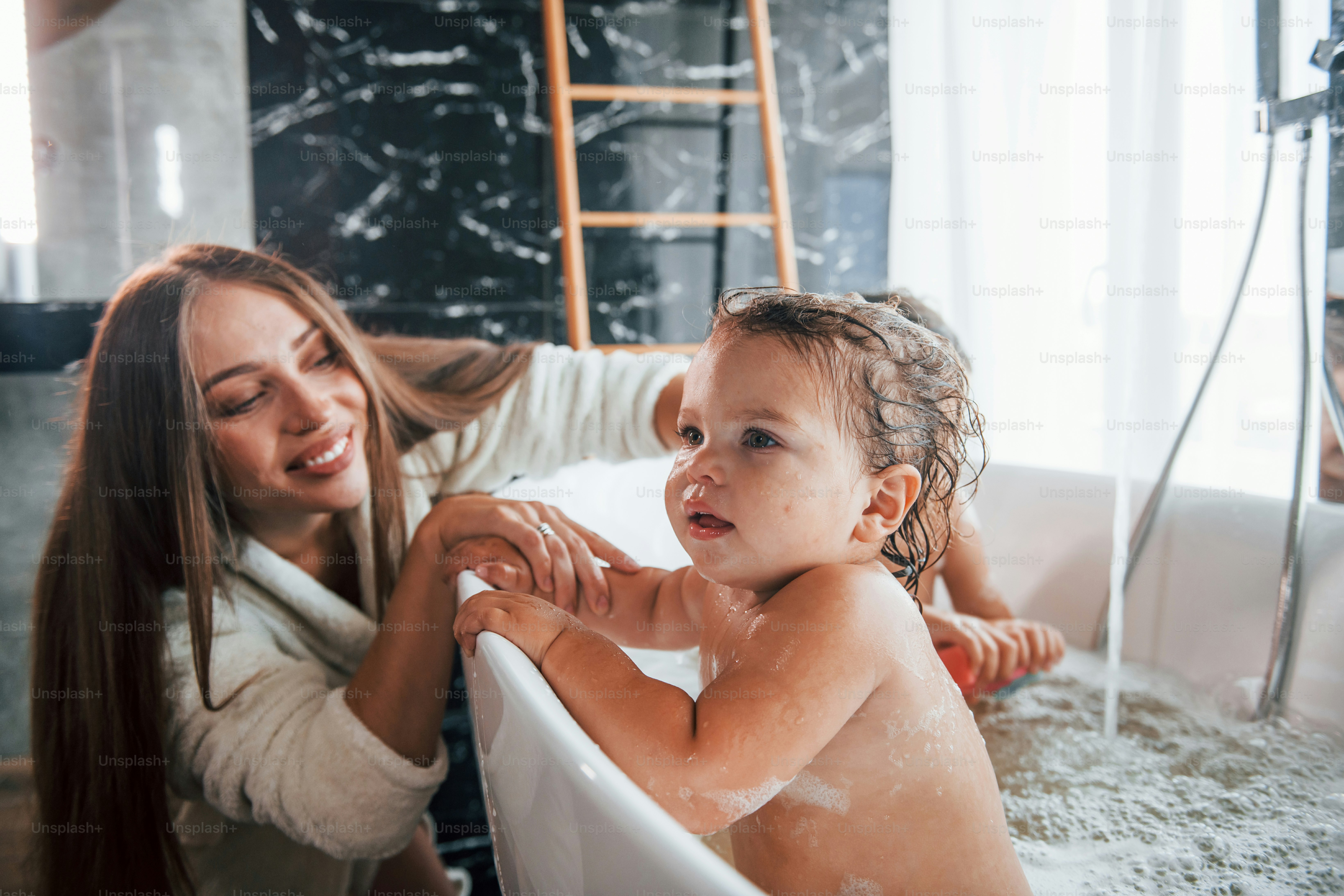 Young mother helps her son and daughter. Two kids washing in the bath ...