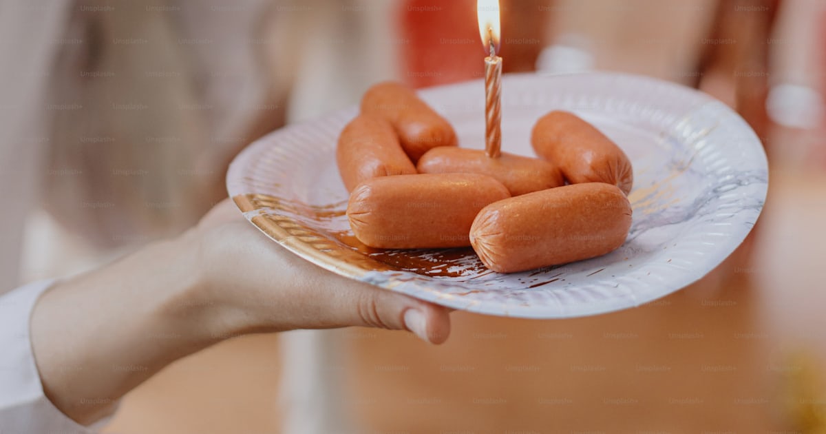 개 생일 파티 행복한 젊은 여성과 배고픈 개는 분홍색 화환을 배경으로 소시지 케이크와 촛불로 생일을 축하합니다 사랑스러운