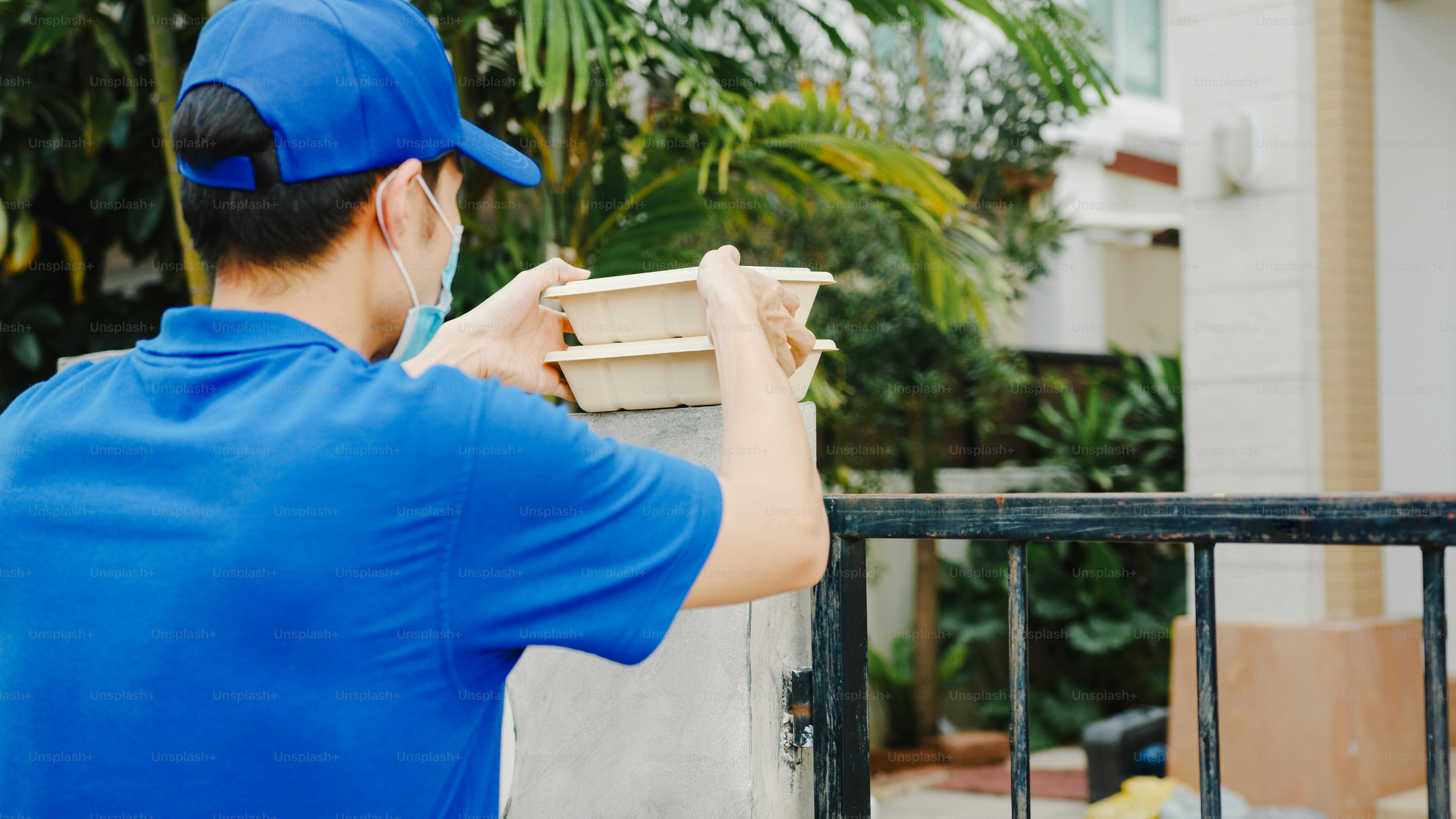 Young postal delivery courier man wear face mask handling food box for send to customer at house ...