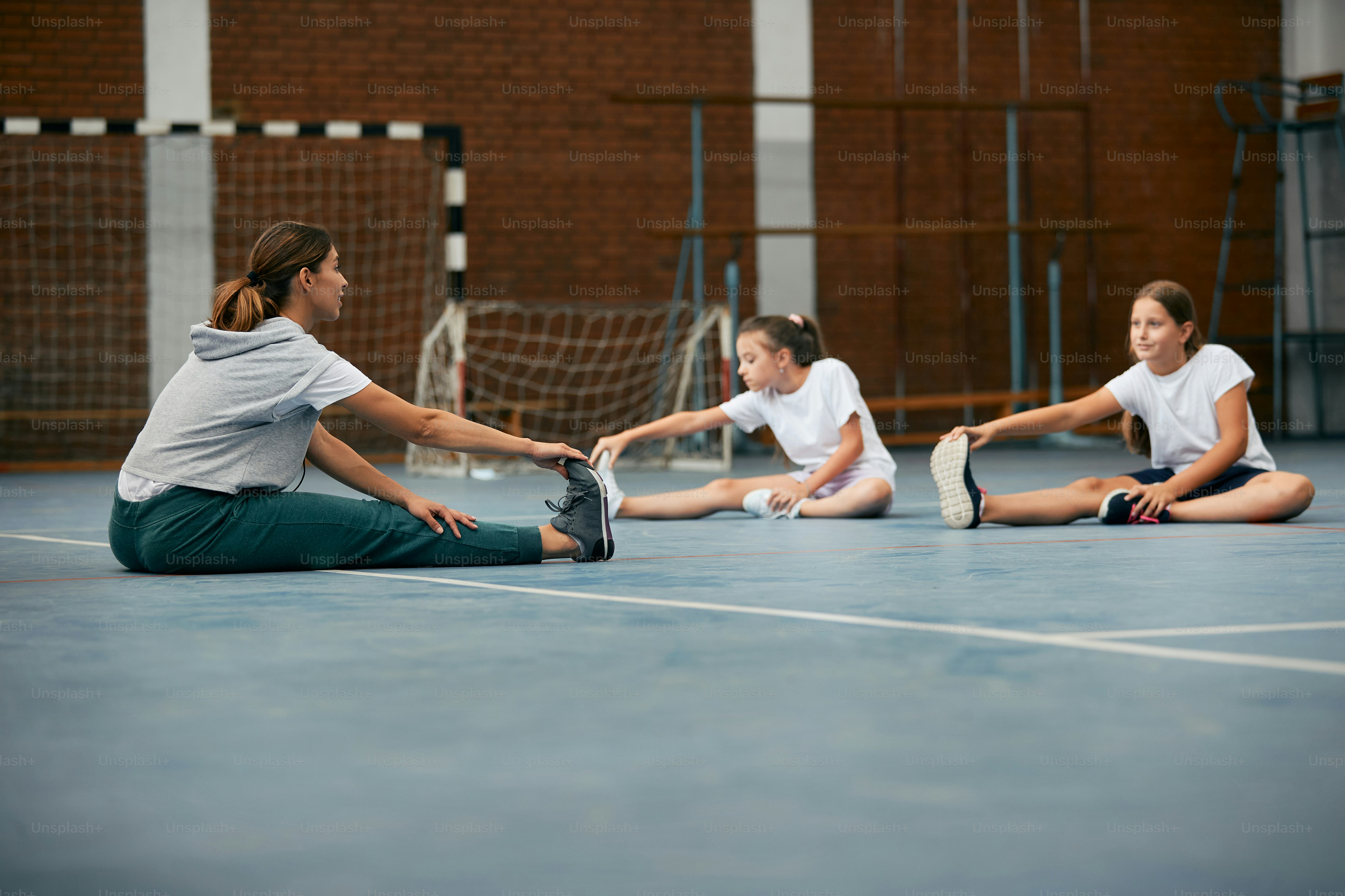 PE teacher and her students warming up and stretching their legs on a ...