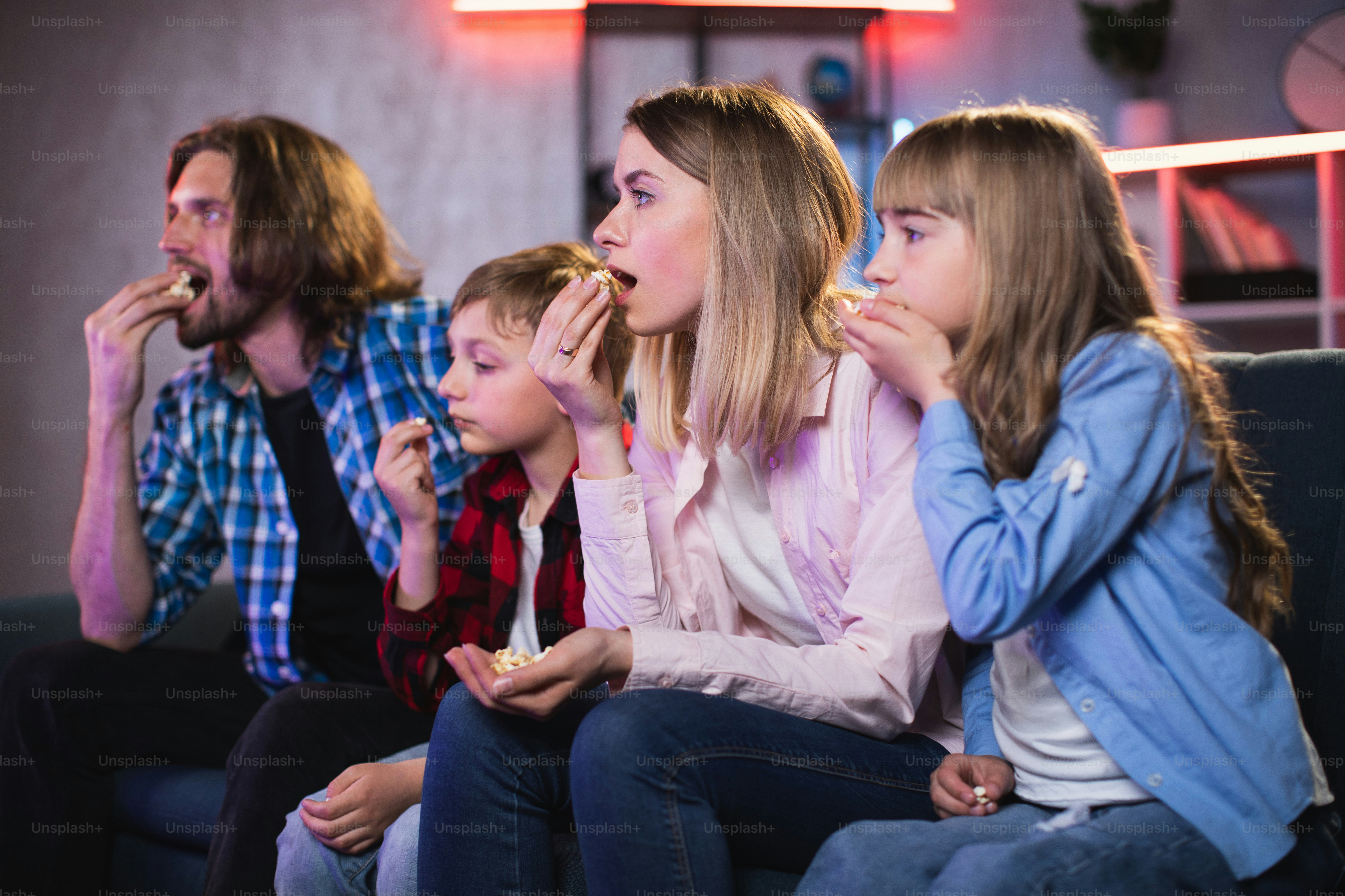 Scared parents with two kids hiding eyes while watching horror movie at ...
