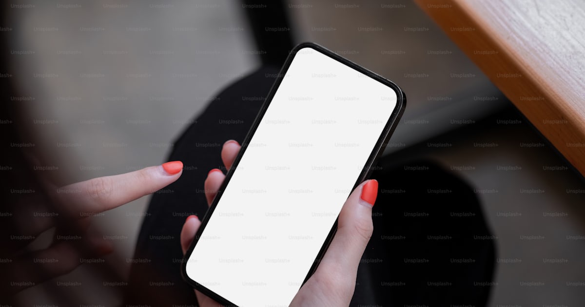 カフェに座っている間、空白の白い画面で黒い携帯電話を保持している女性のトップビューのモックアップ画像の写真 写真撮影 Unsplashの写真