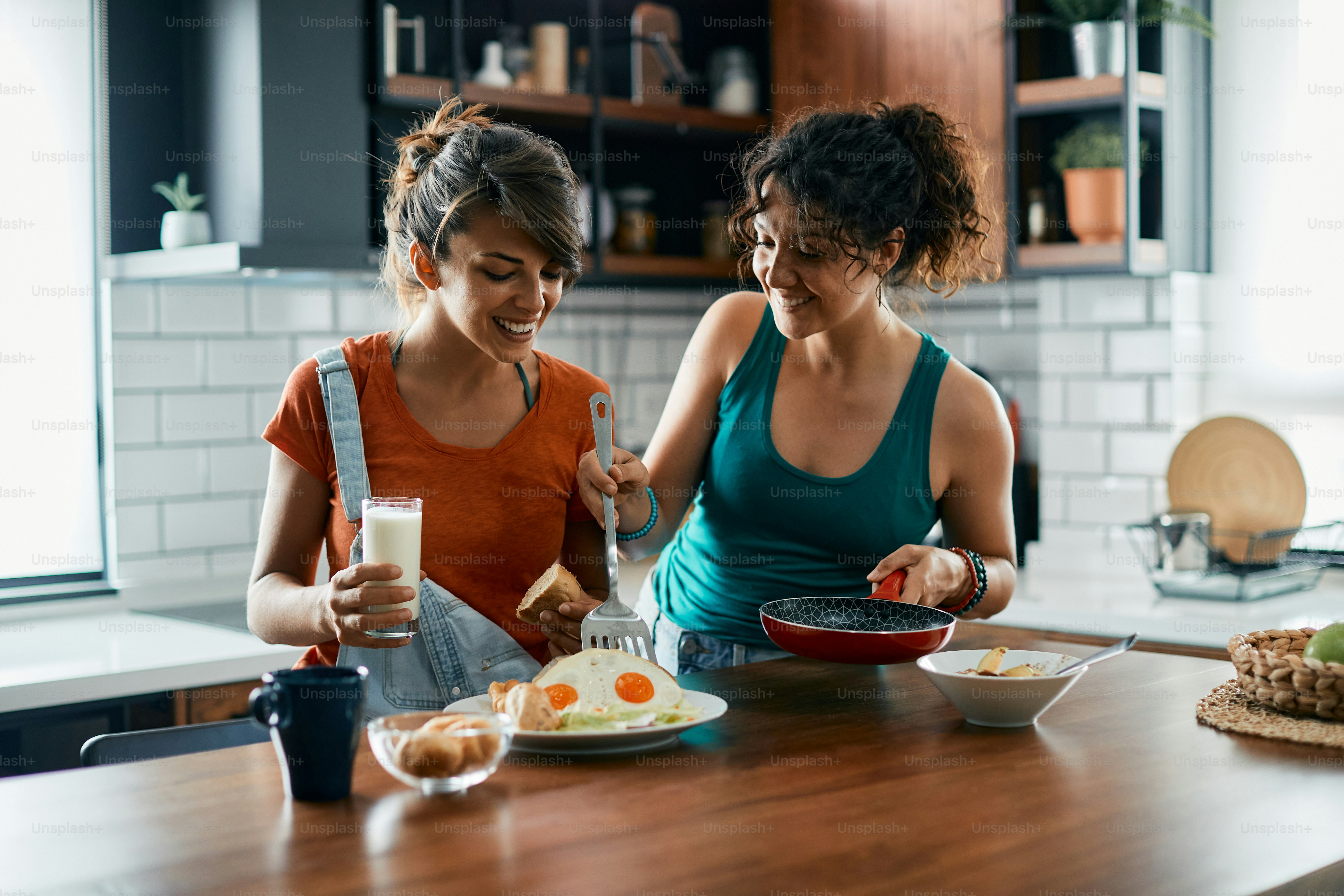 Happy lesbian woman serving breakfast to her girlfriend at dining table ...