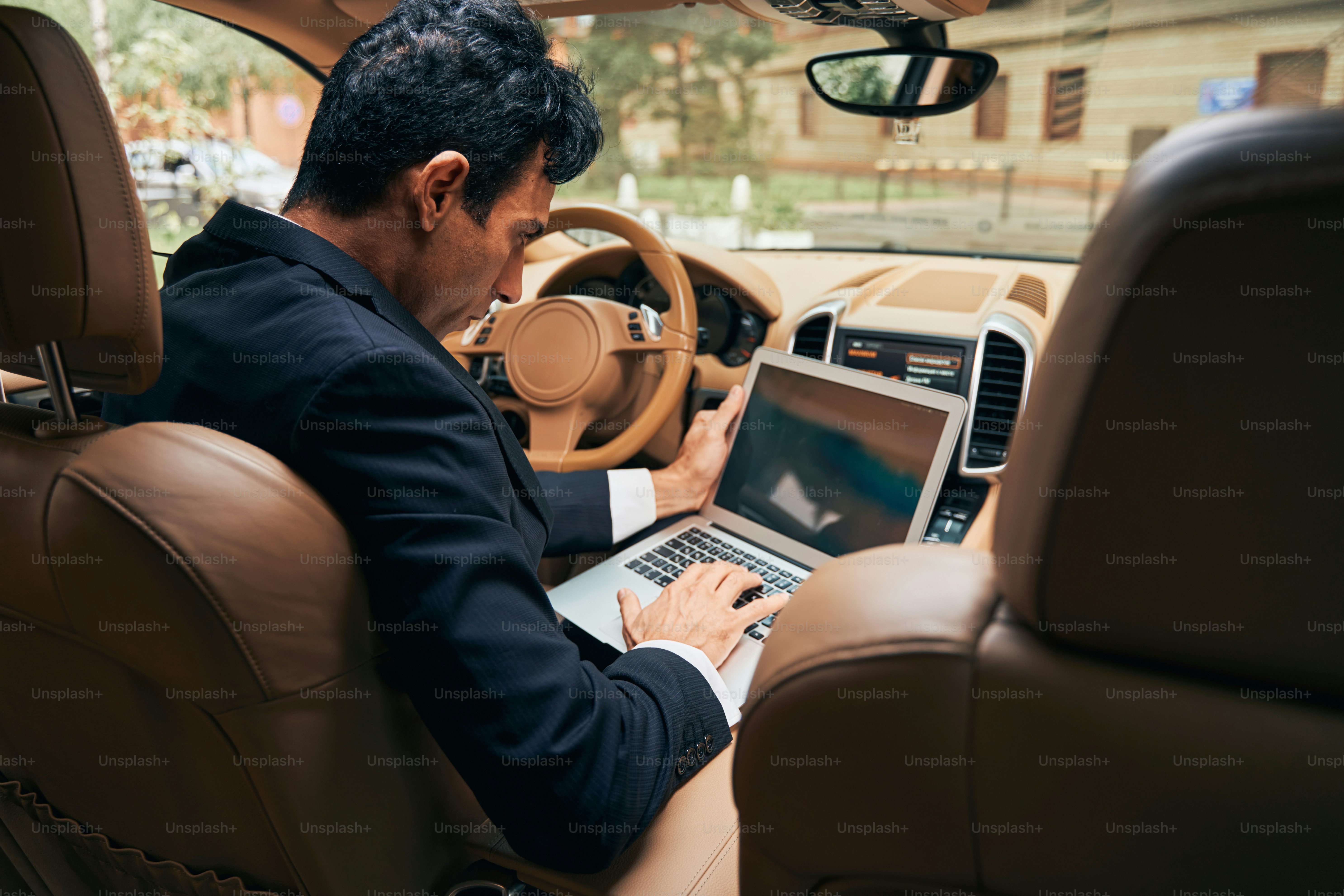 View from car rear seat of man using laptop and clicking on keyboard ...