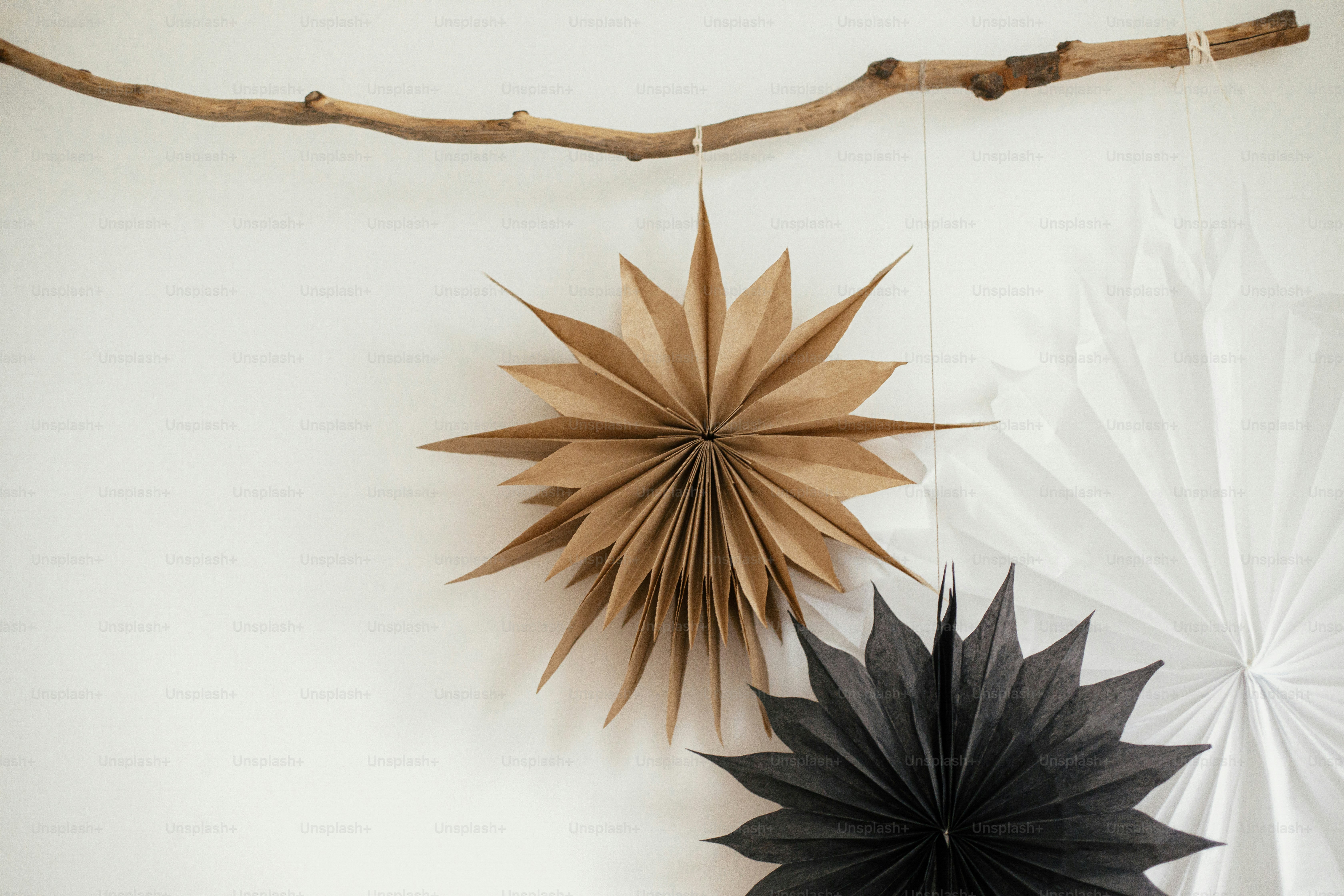 Stylish Christmas stars hanging from wooden branch on white wall ...