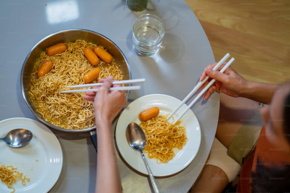 아름다운 아시아 여자 친구들은 소시지와 함께 인스턴트 라면을 먹고 밤에 거실에서 함께 이야기합니다 여성 커플 여자 친구는