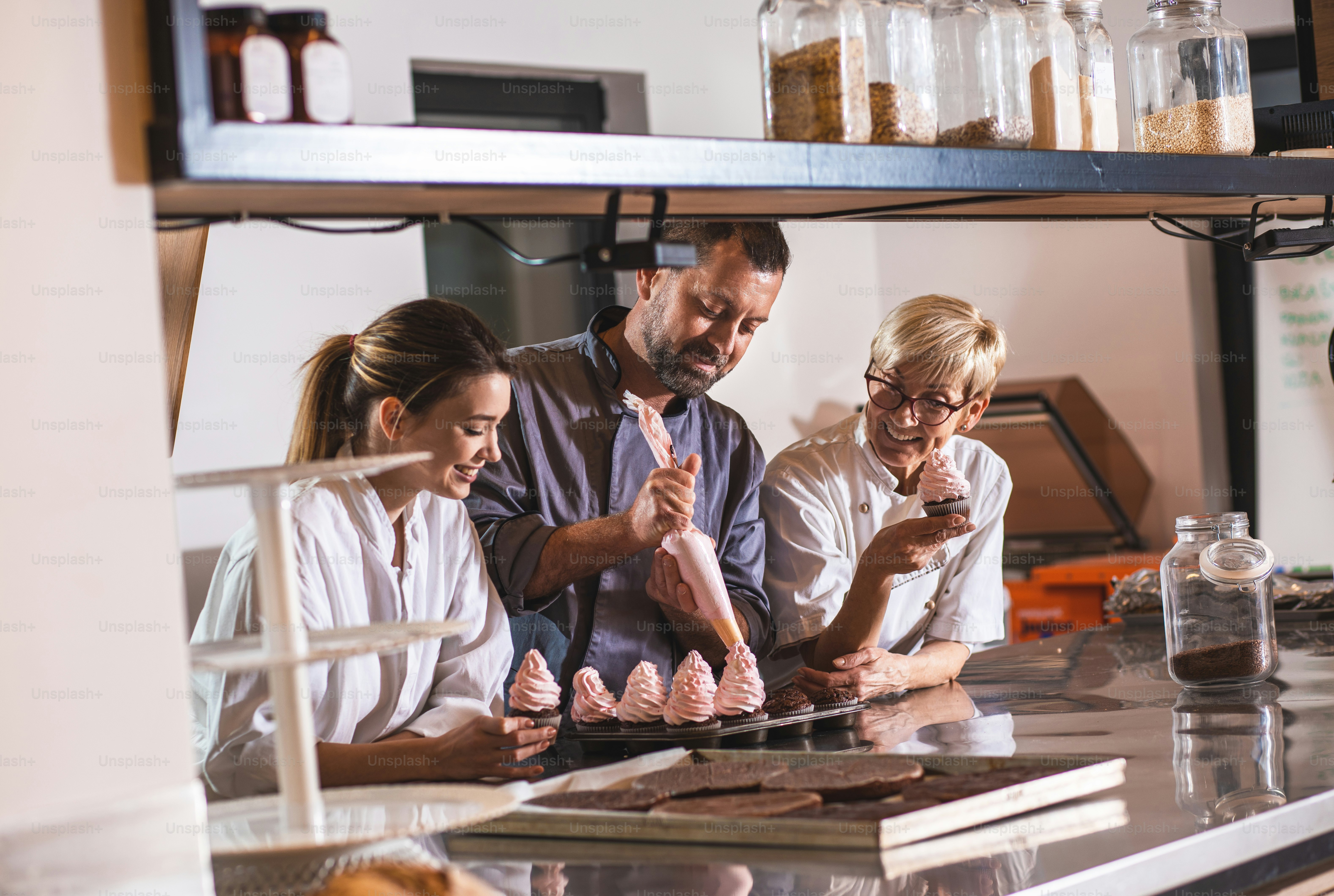 Group of bakers in uniform decorating desserts in modern manufacturing ...