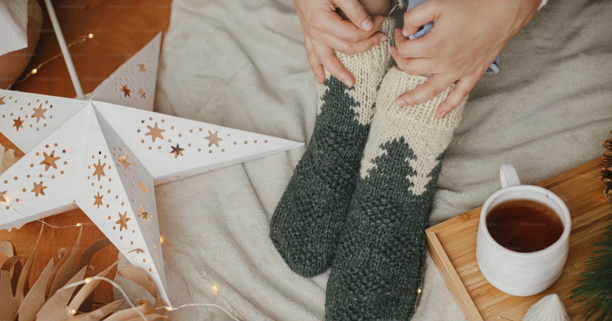 自宅での居心地の良い冬のひととき。温かいお茶、クリスマスの星、金色の光、木、ろうそくのある柔らかいベッドの上の毛糸の靴下の女性の足