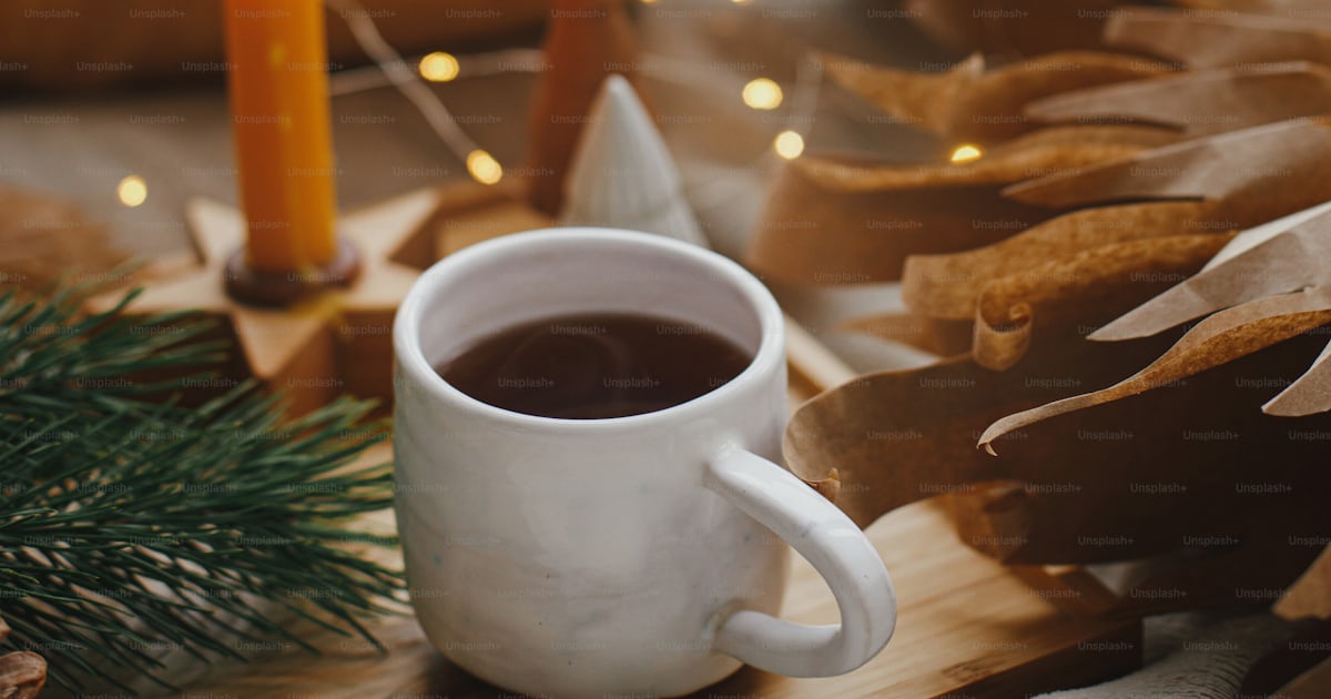 照らされたクリスマススター、クリスマスライト、松の木、ろうそく、窓のベッドの枕の背景に温かいお茶。居心地の良いスカンジナビアの家。冬のヒュッゲ