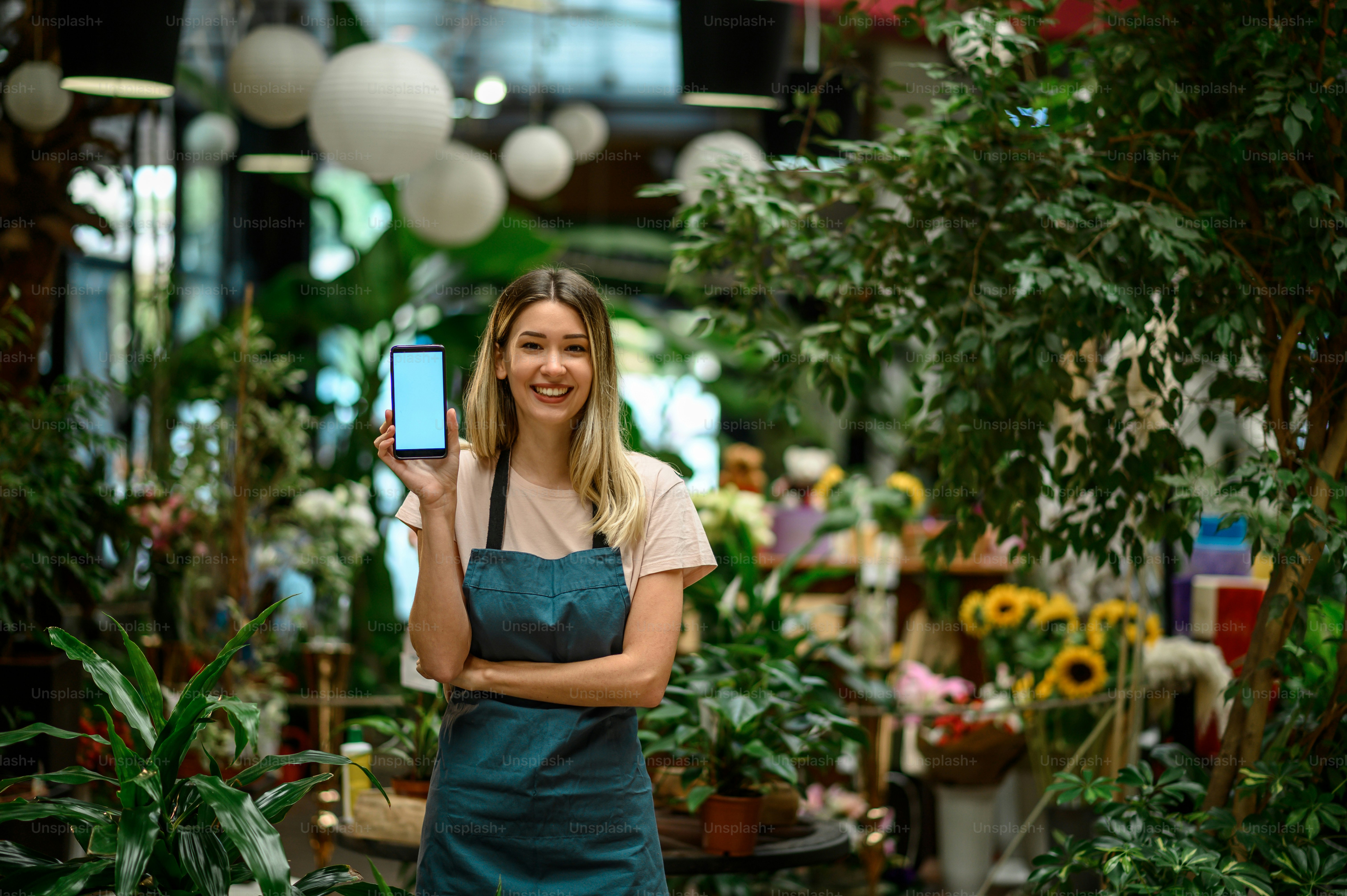 Florist showing a smartphone while surrounded with flowers and plants ...