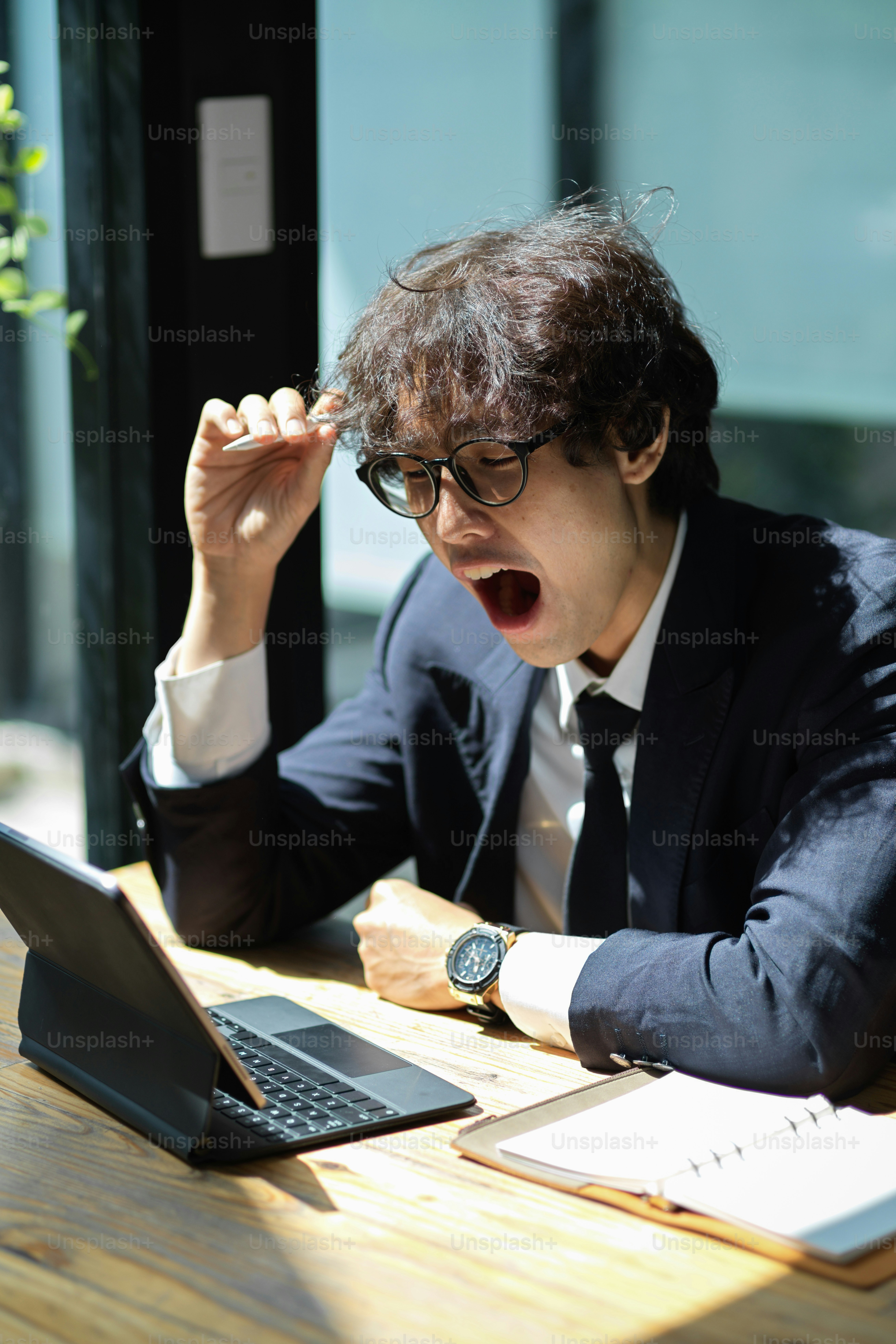 Tired salaryman works on his digital tablet computer and feels sleepy ...