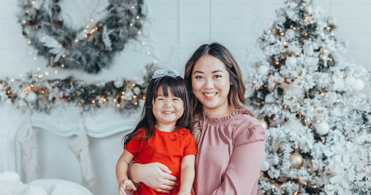 クリスマスや新年を祝う娘の幼児の女の子を持つアジアの家族の母親。クリスマス ツリーの家のそばに立っている子供と混血のお母さん。冬休みのお祝い
