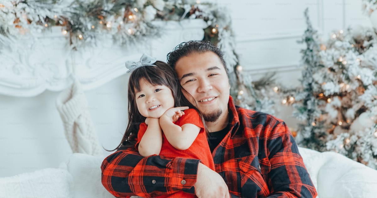 クリスマスや新年を祝う娘の幼児の女の子と抱き合うアジアの家族の父の父。ソファ ソファに座って、家で寄り添う子供と混血のお父さんの男。冬休みのお