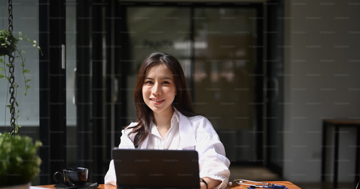 흰색 의료 유니폼을 입은 긍정적인 여성 의사가 직장에 앉아 카메라를 향해 웃고 있다 사진 Unsplash의 태국 이미지