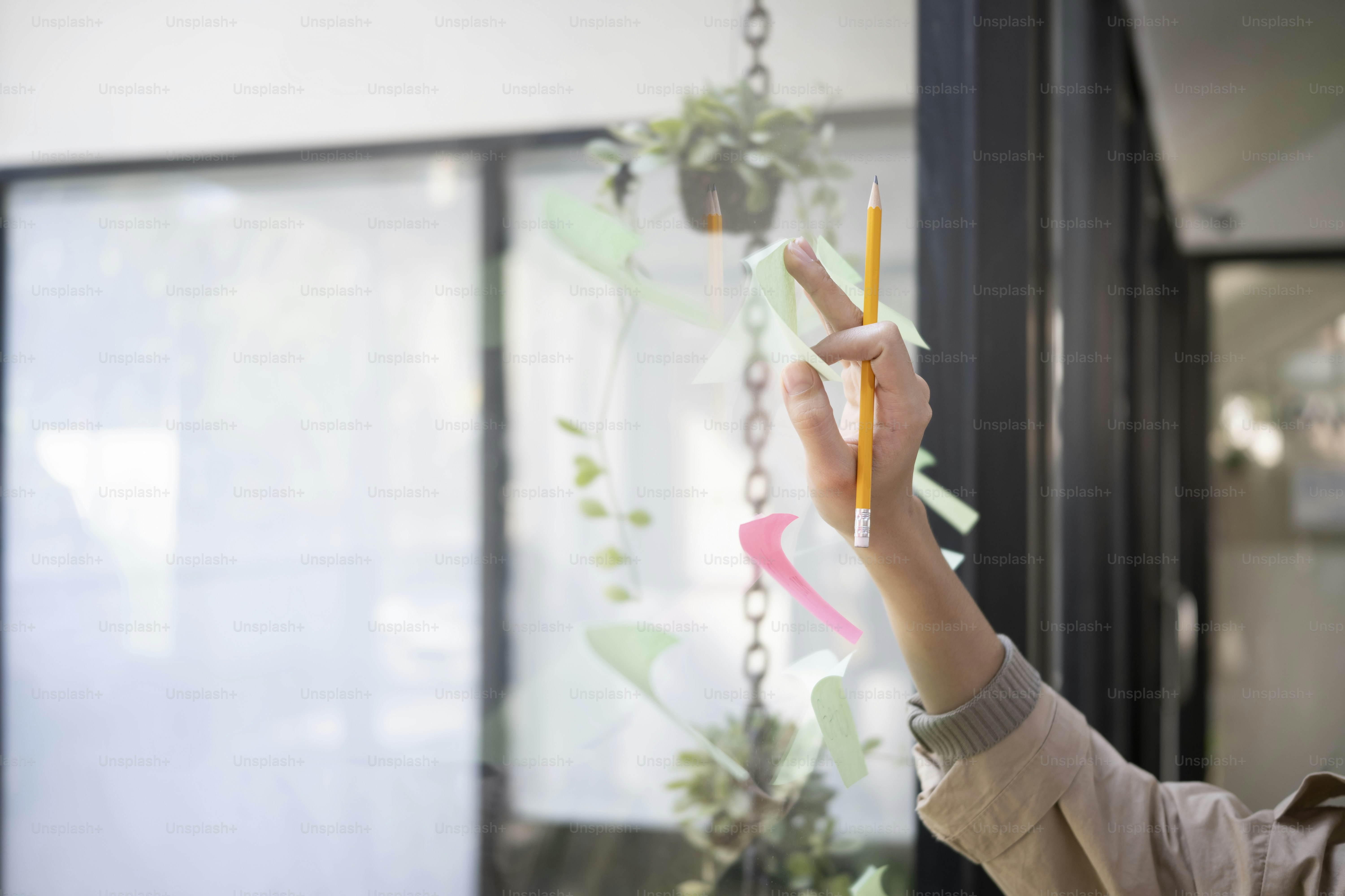 Cropped shot female designer putting colorful sticky note on a glass ...