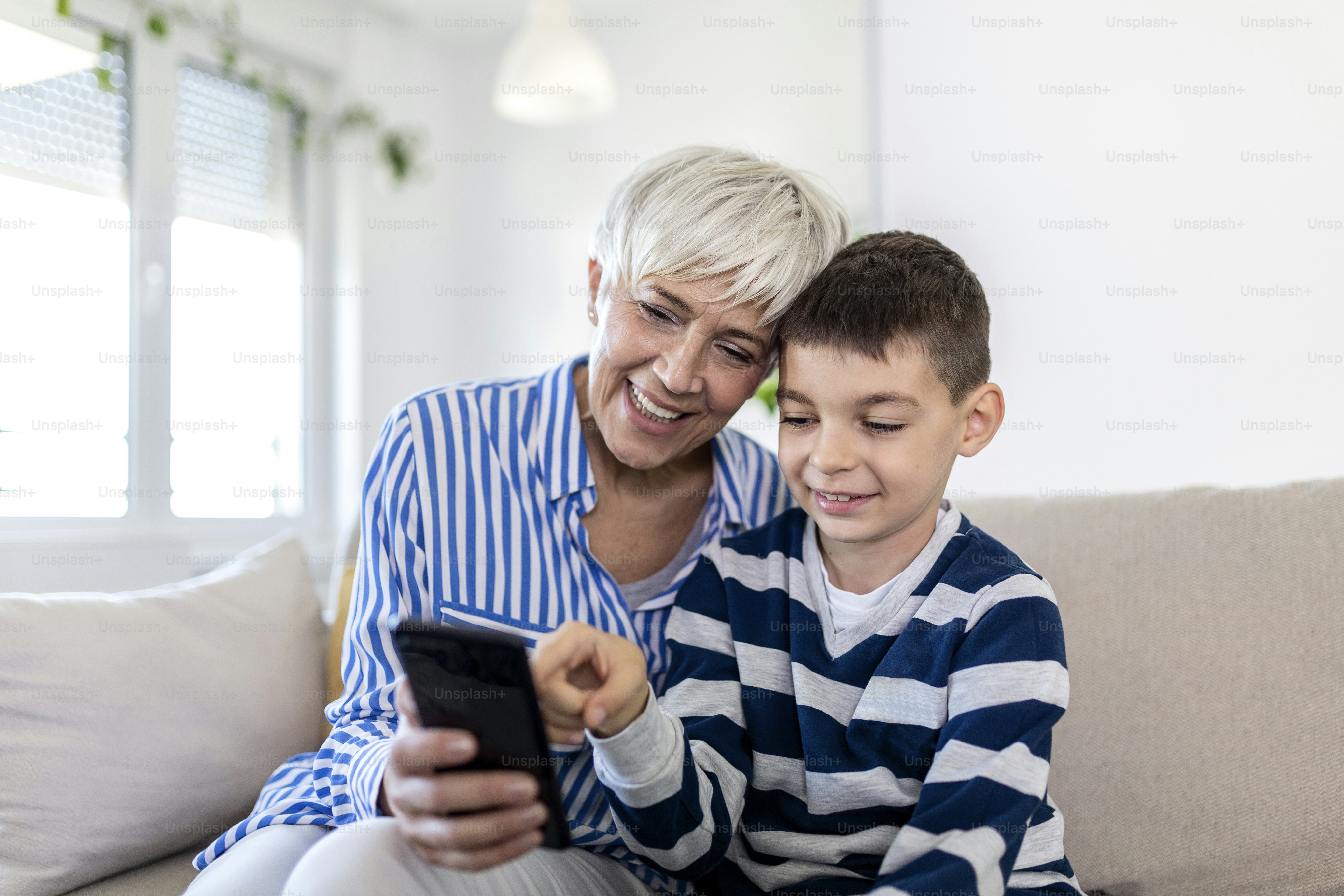 Happy grandmother and grandson using tablet together, sitting on cozy ...