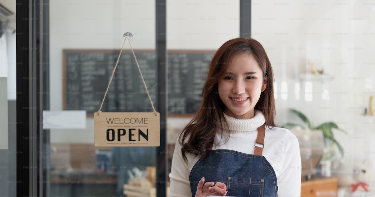 열린 간판이 있는 카페 카운터 뒤에 서 있는 웃는 아시아 기업가의 초상화 사진 Unsplash의 사업 이미지