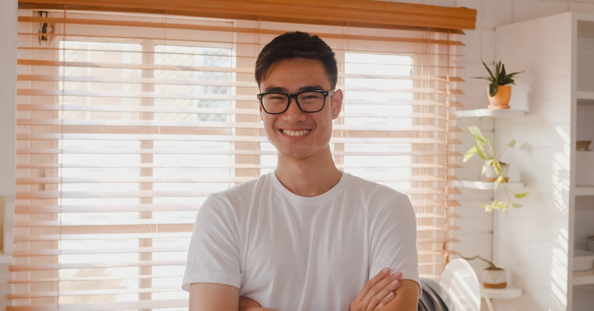 행복한 젊은 아시아 남성은 행복한 미소를 짓고 팔짱을 끼고 집에서 부엌에서 휴식을 취하는 동안 카메라를 바라보고 있다 사진