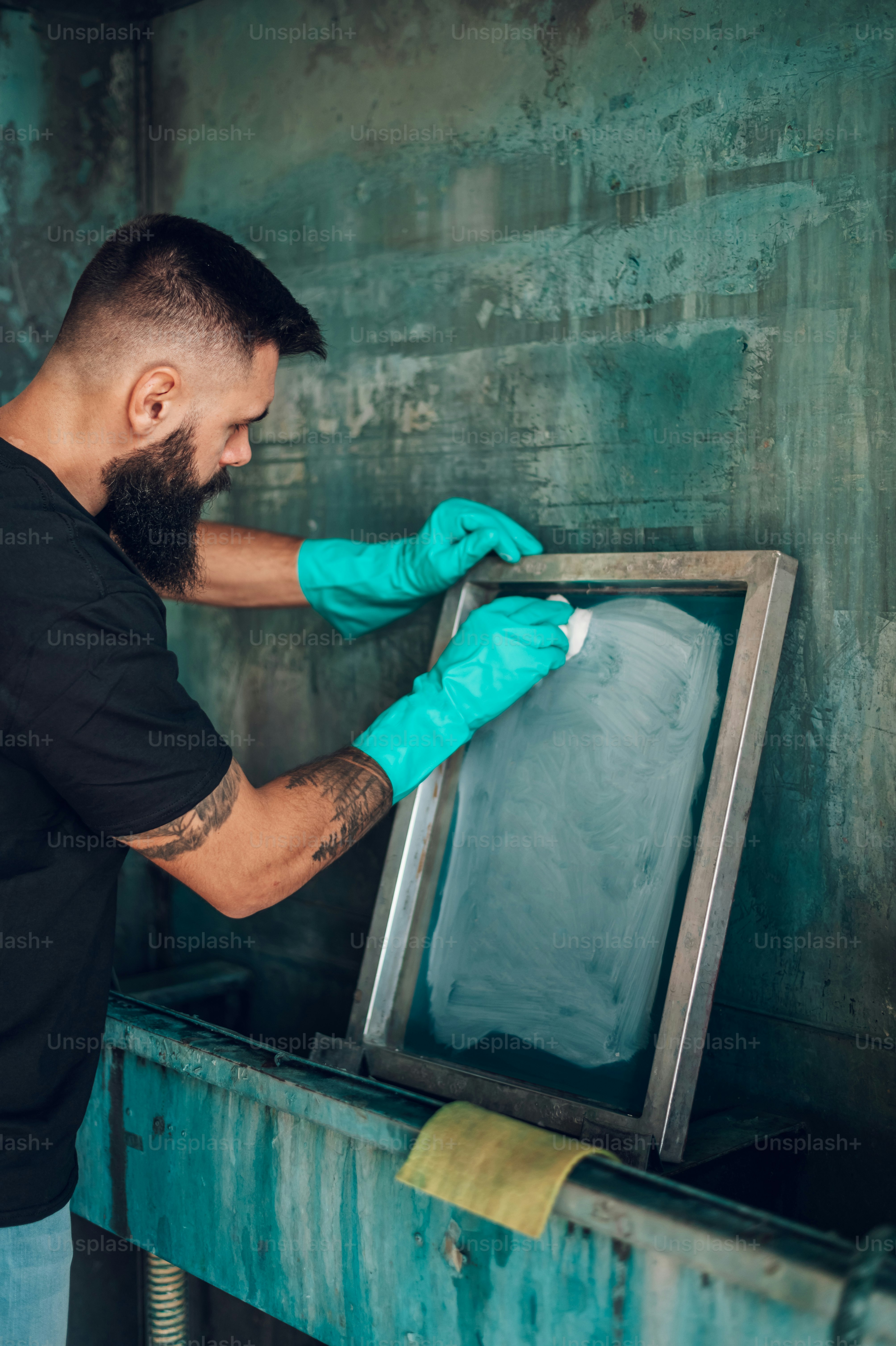 Male worker cleaning screen frame with a cloth in a printing workshop ...
