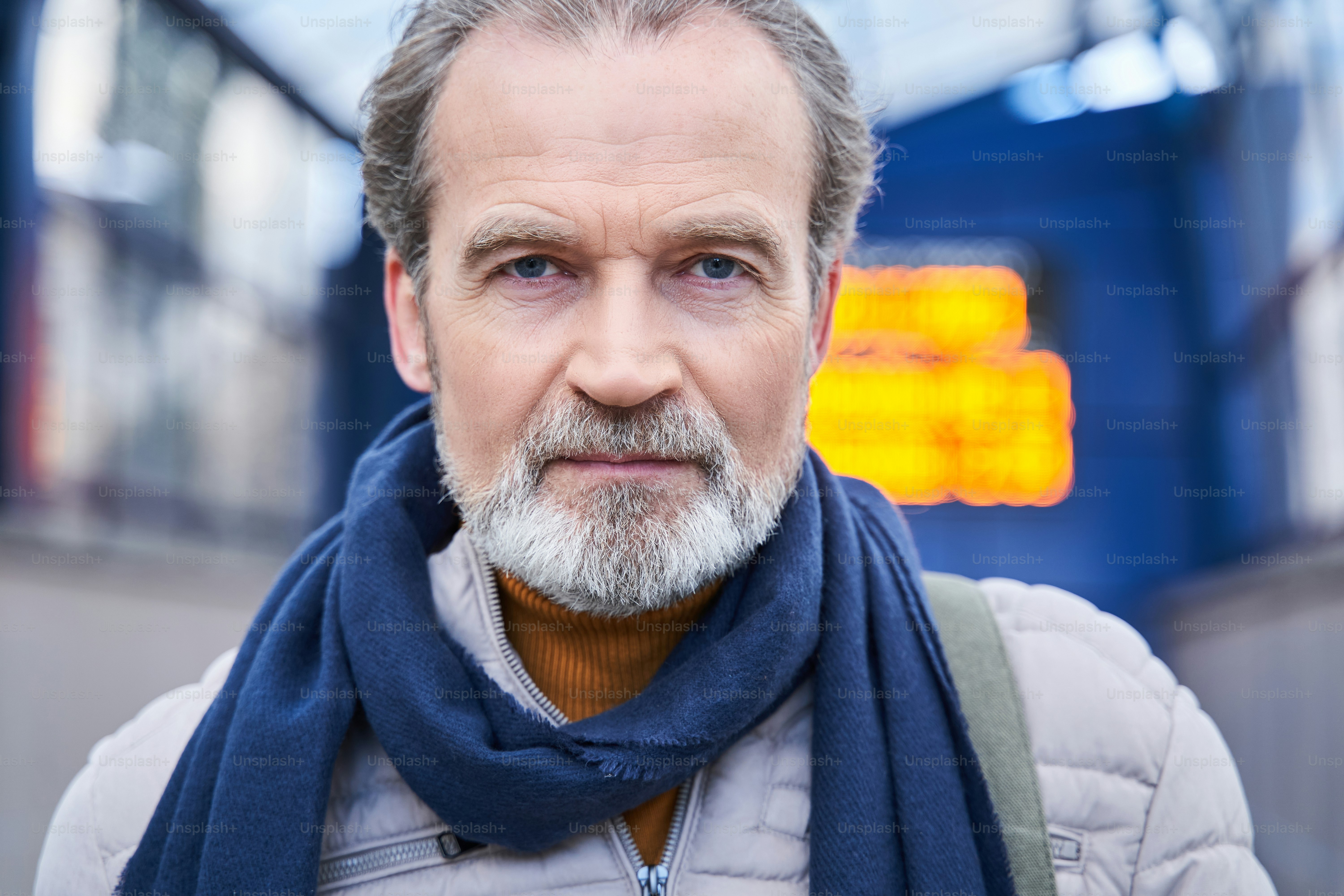 Portrait of mindful grey haired male wearing scarf walking on street ...