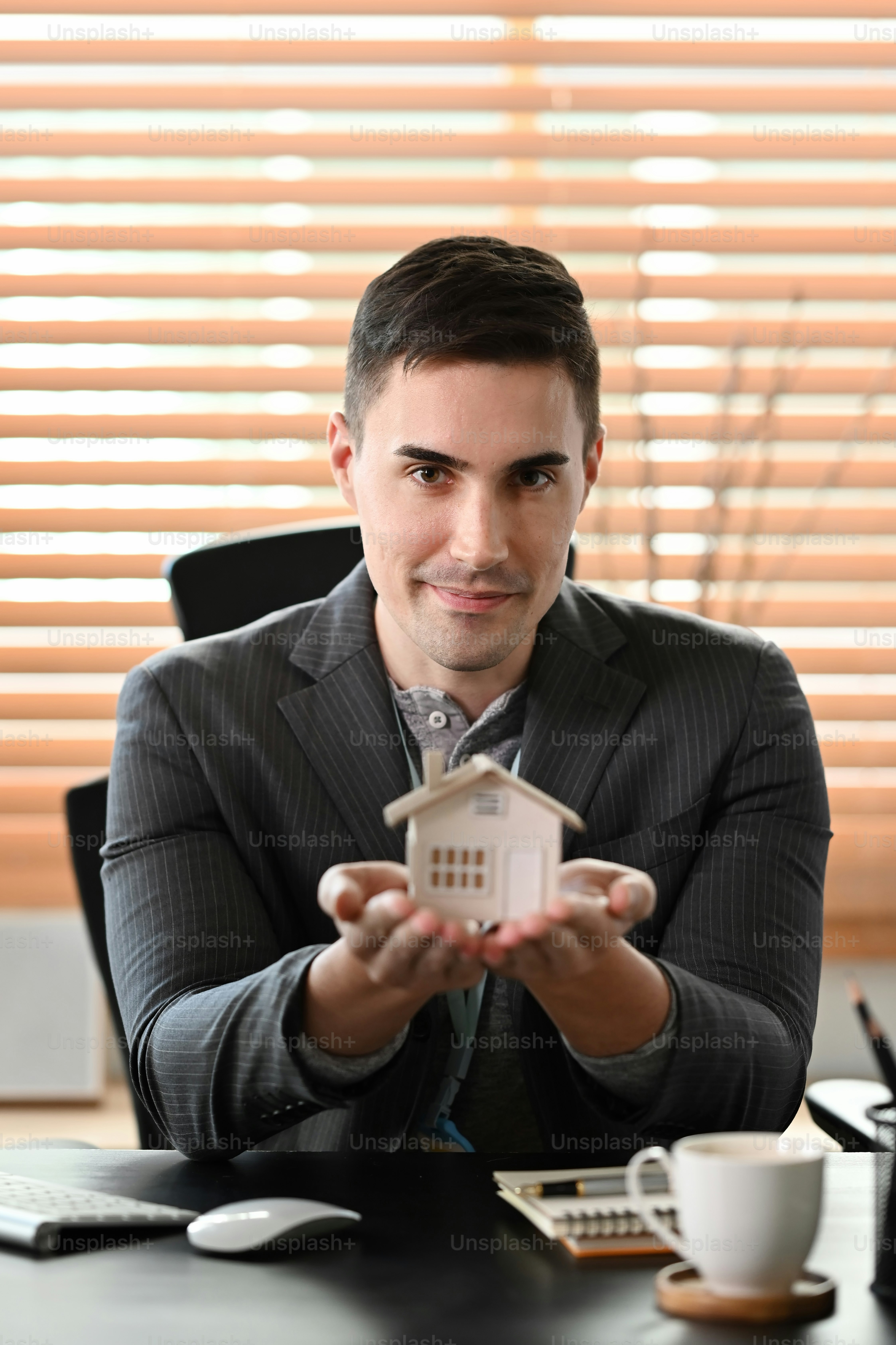 Portrait of real estate agent holding small house model and looking at ...