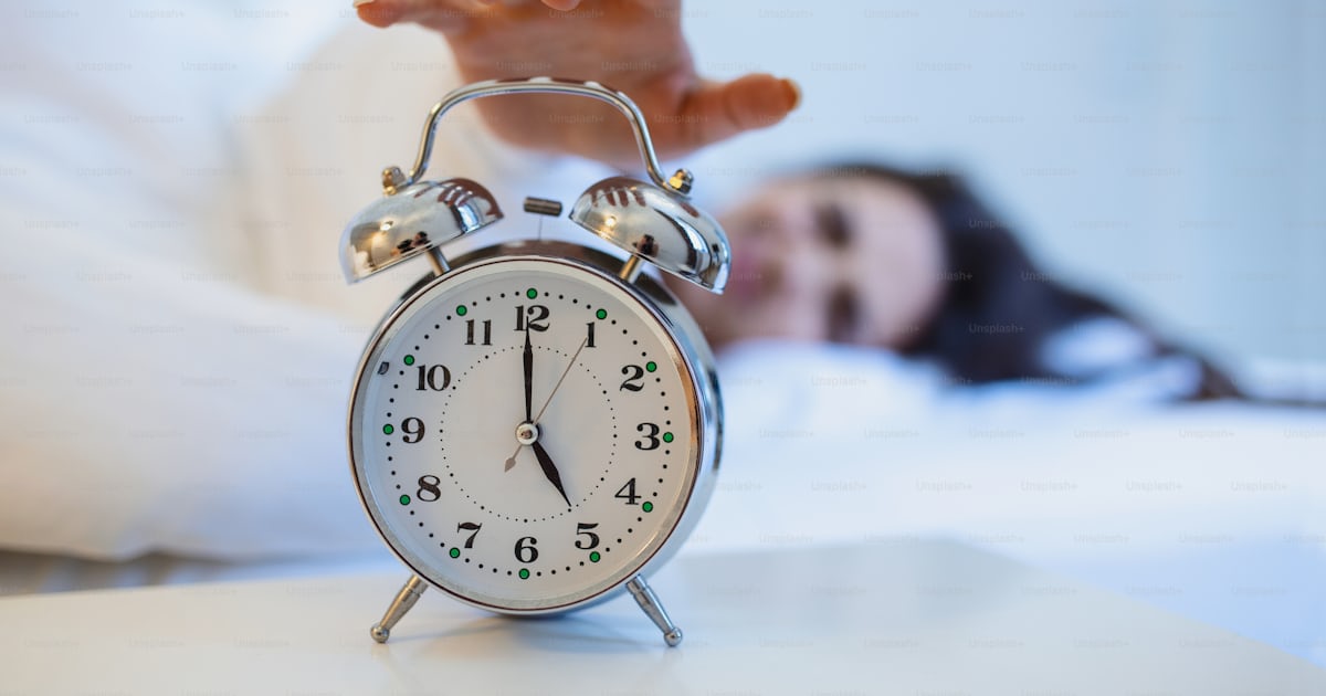 Frau liegt im Bett und schaltet morgens um 5 Uhr morgens einen Wecker ... Frau liegt im Bett und schaltet morgens um 5 Uhr morgens einen Wecker ...