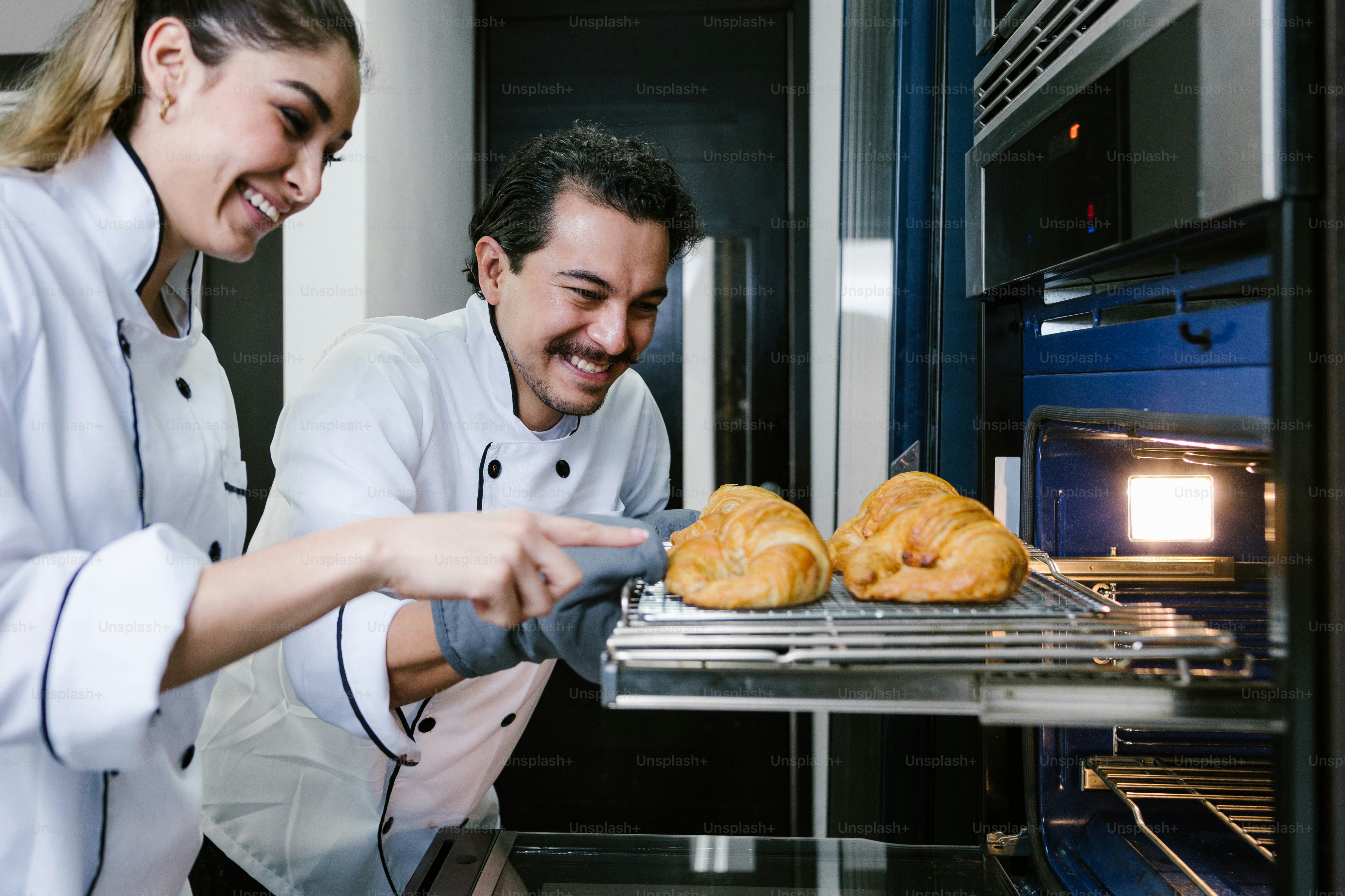 Young Latin couple woman and man bakers and baking croissants and bread ...