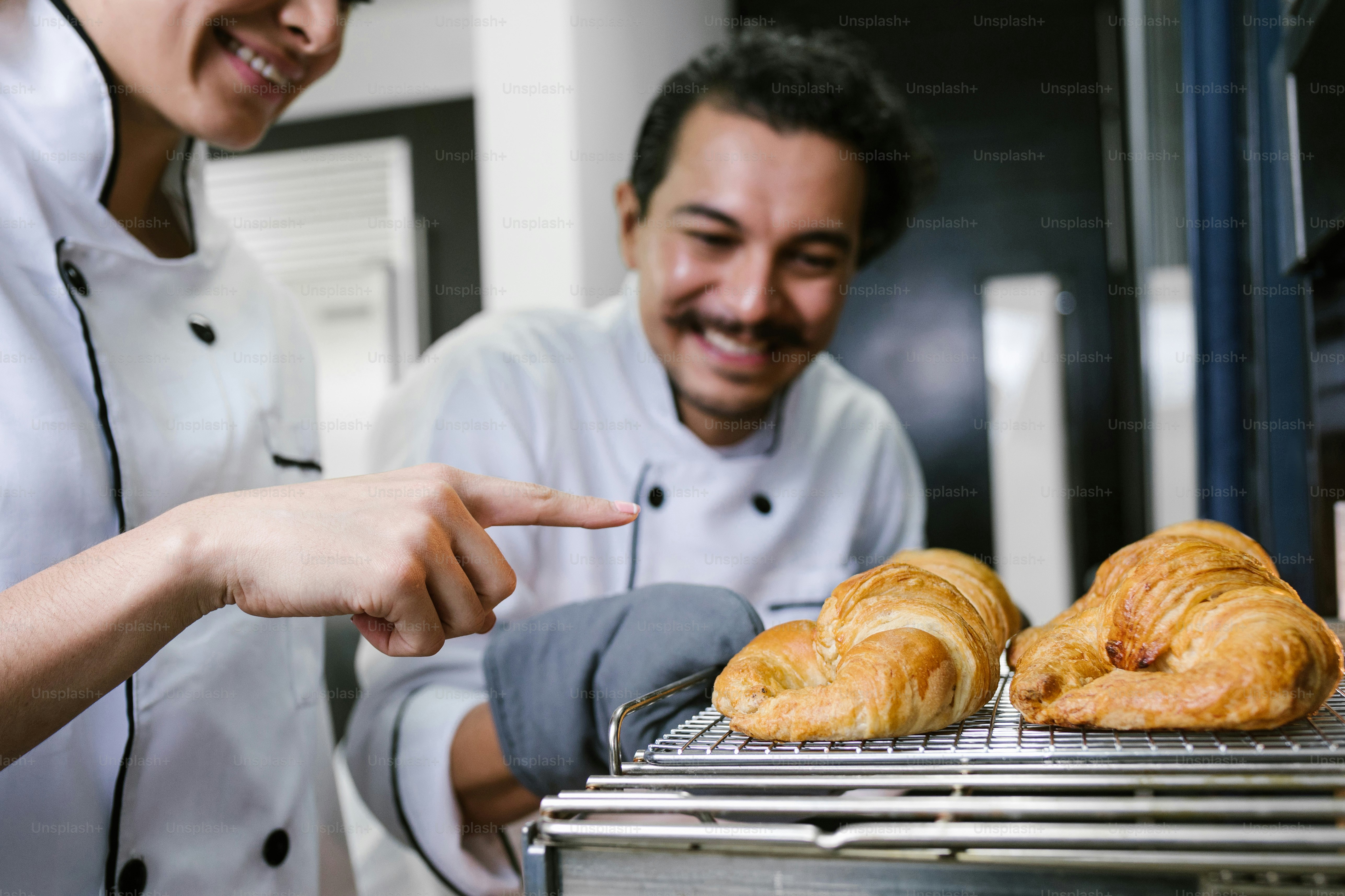 Young Latin man baker and baking croissant and bread on oven at kitchen ...
