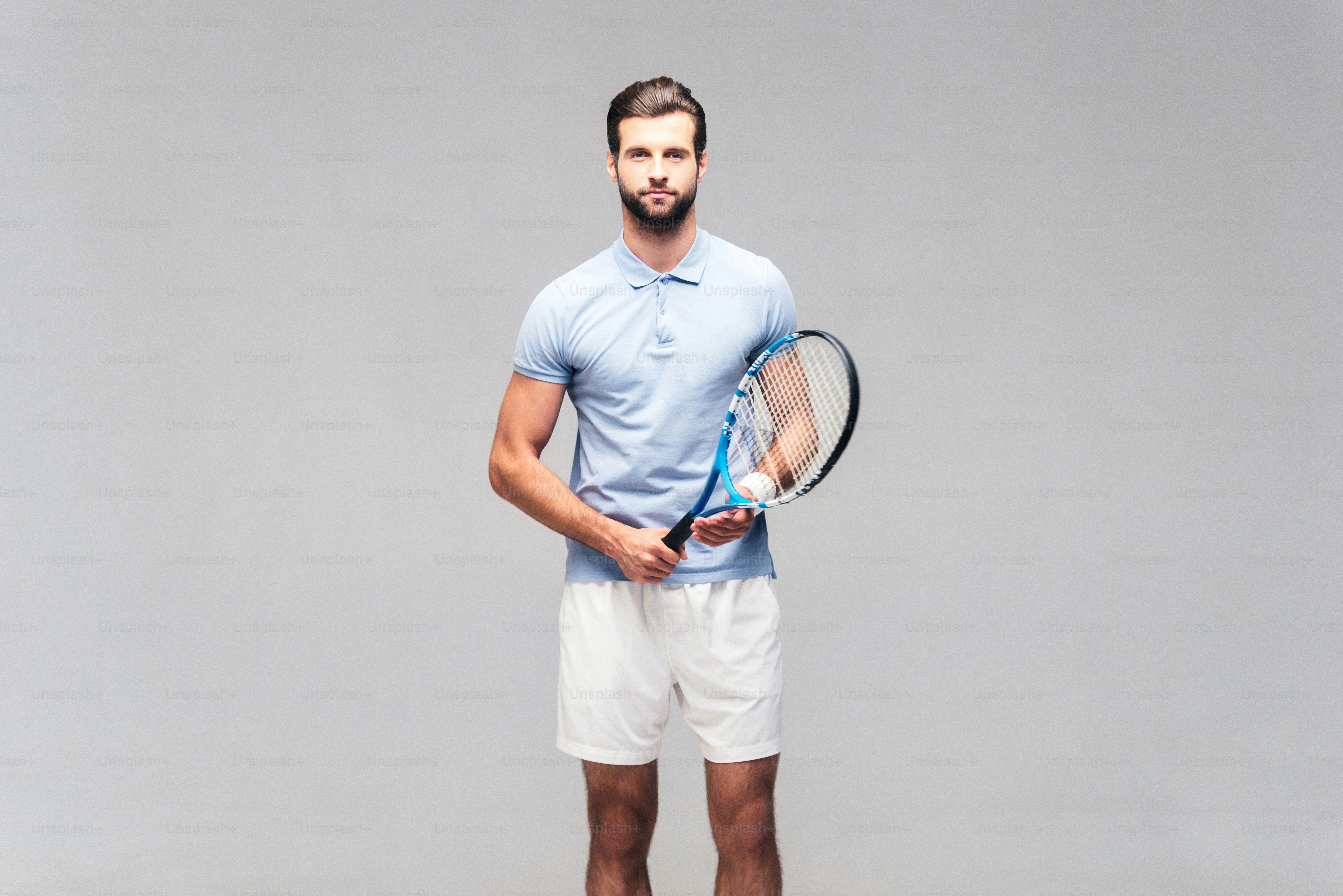 Handsome young man in sports clothing carrying tennis racket and ...