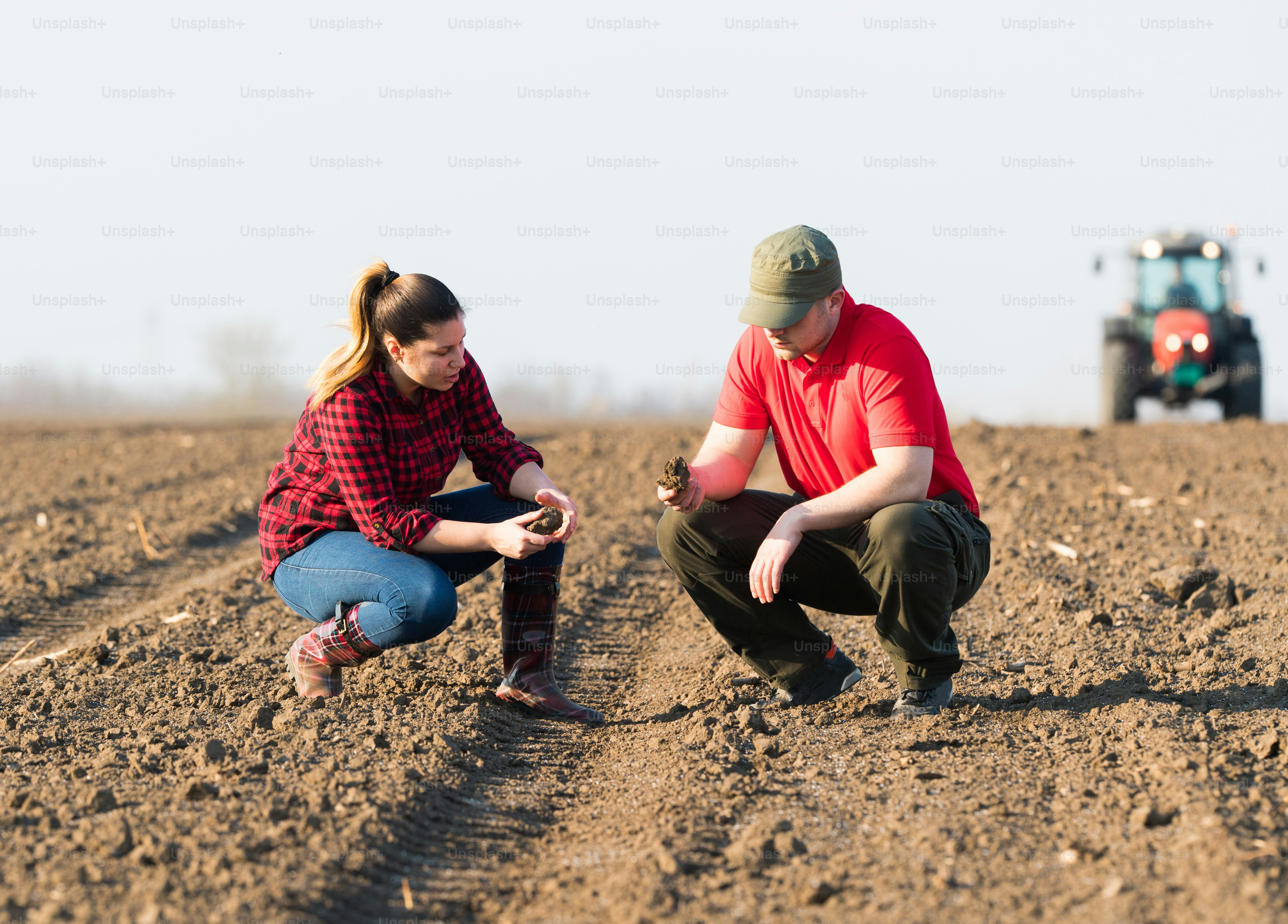 Young farmers examing dirt while tractor is plowing field photo – Brown ...
