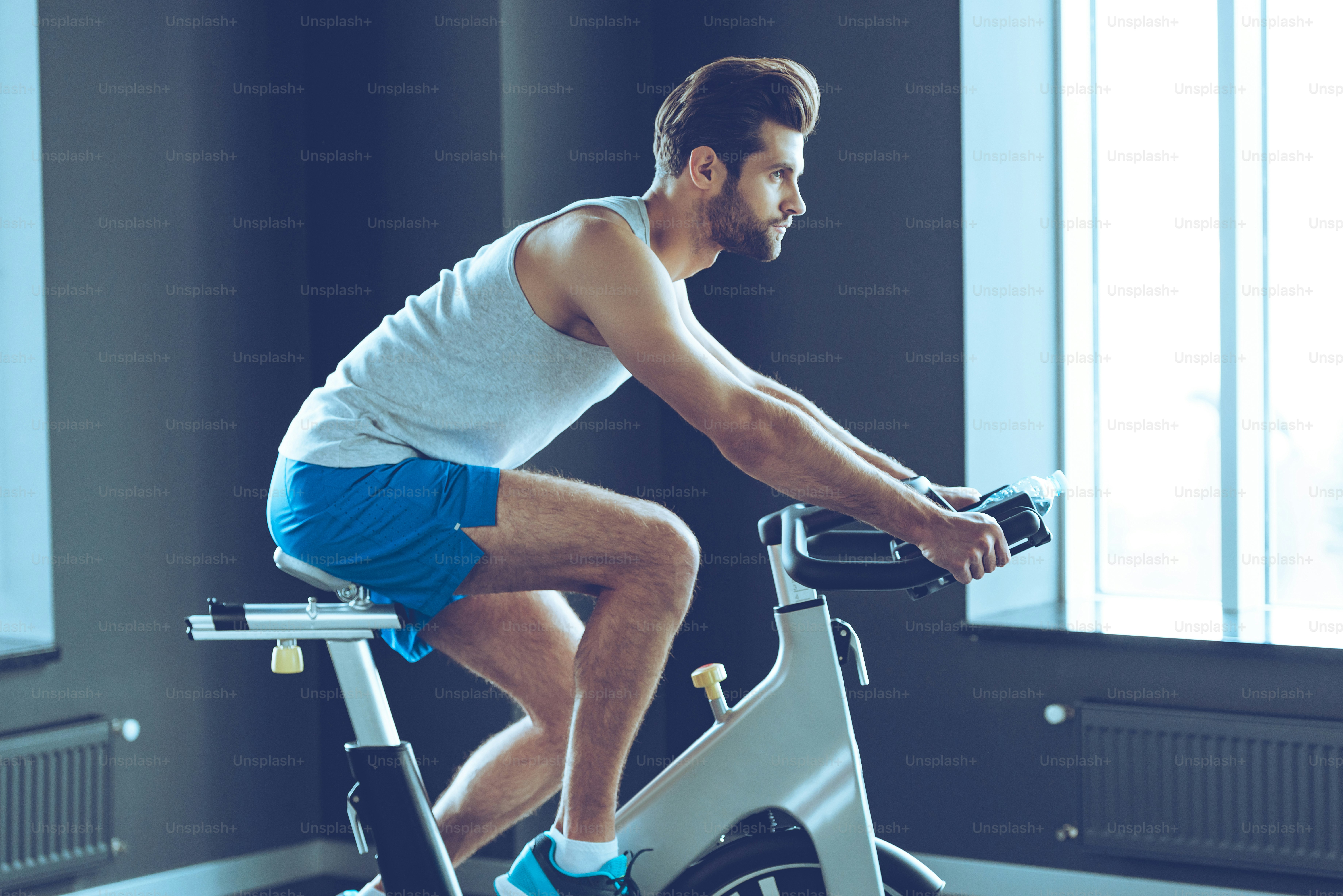Side view of young handsome man in sportswear cycling at gym photo ...