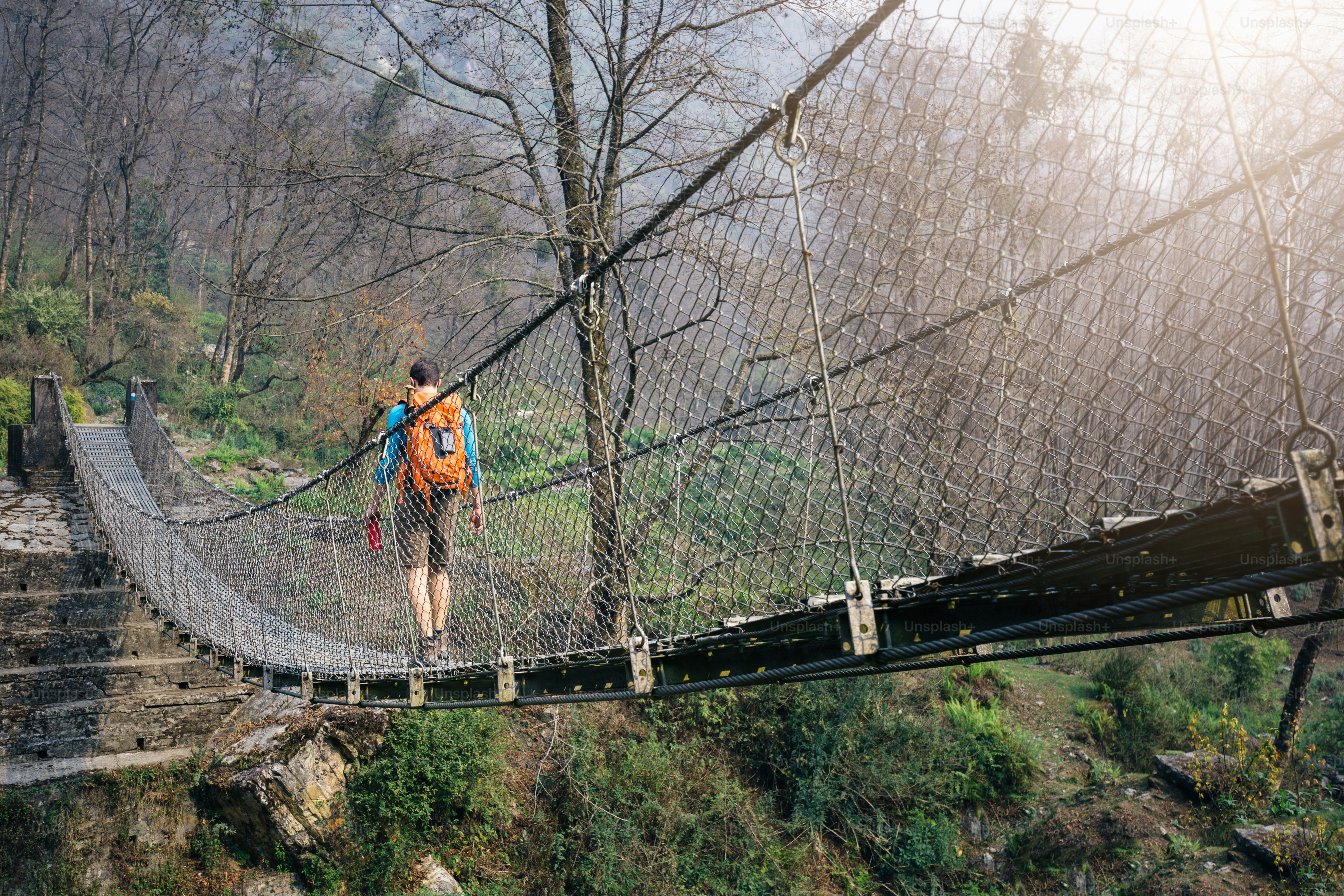 Tourist with backpack crossing suspension footbridge at Himalayas ...