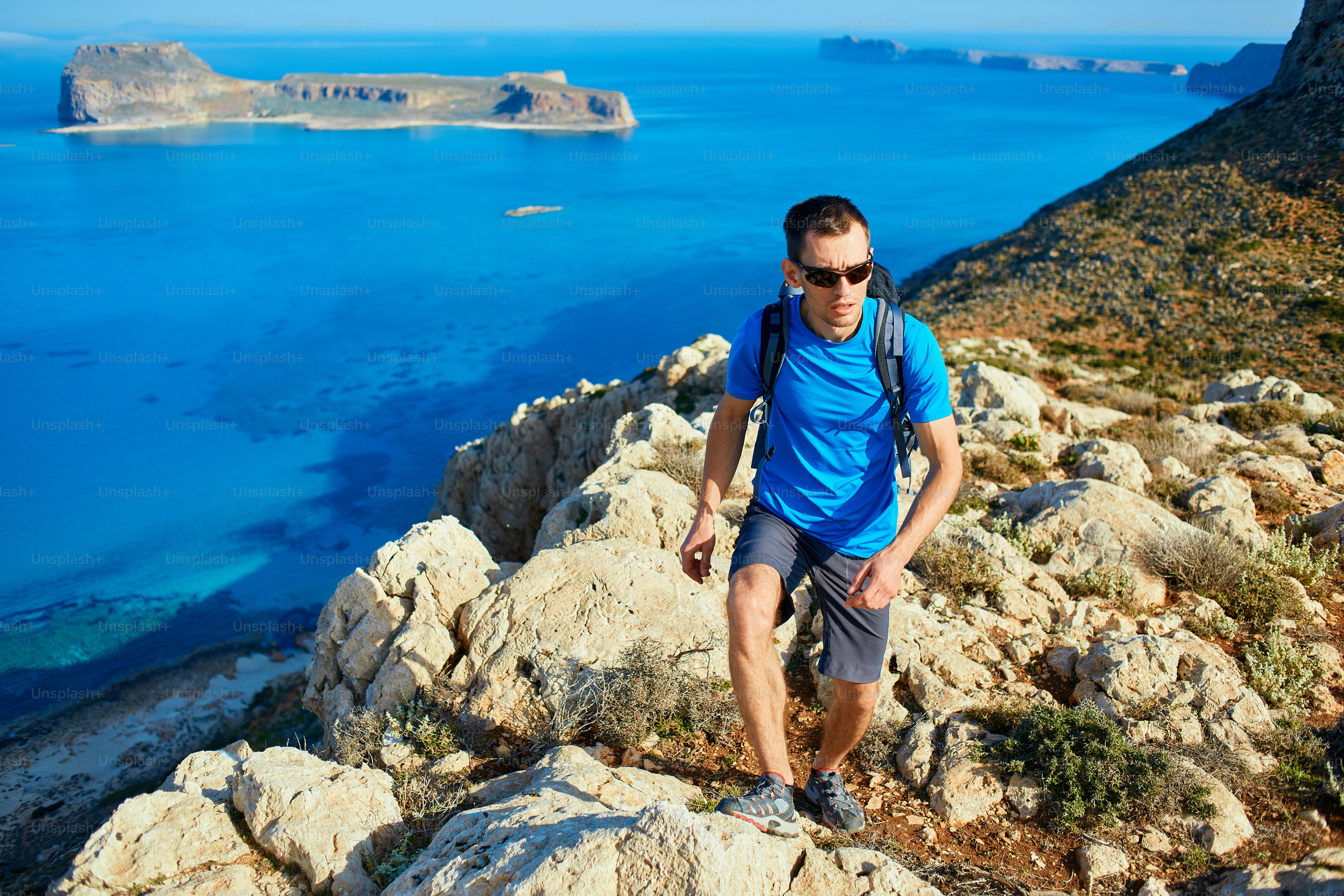 Male traveler with backpack runs on the cliff against sea and blue sky ...