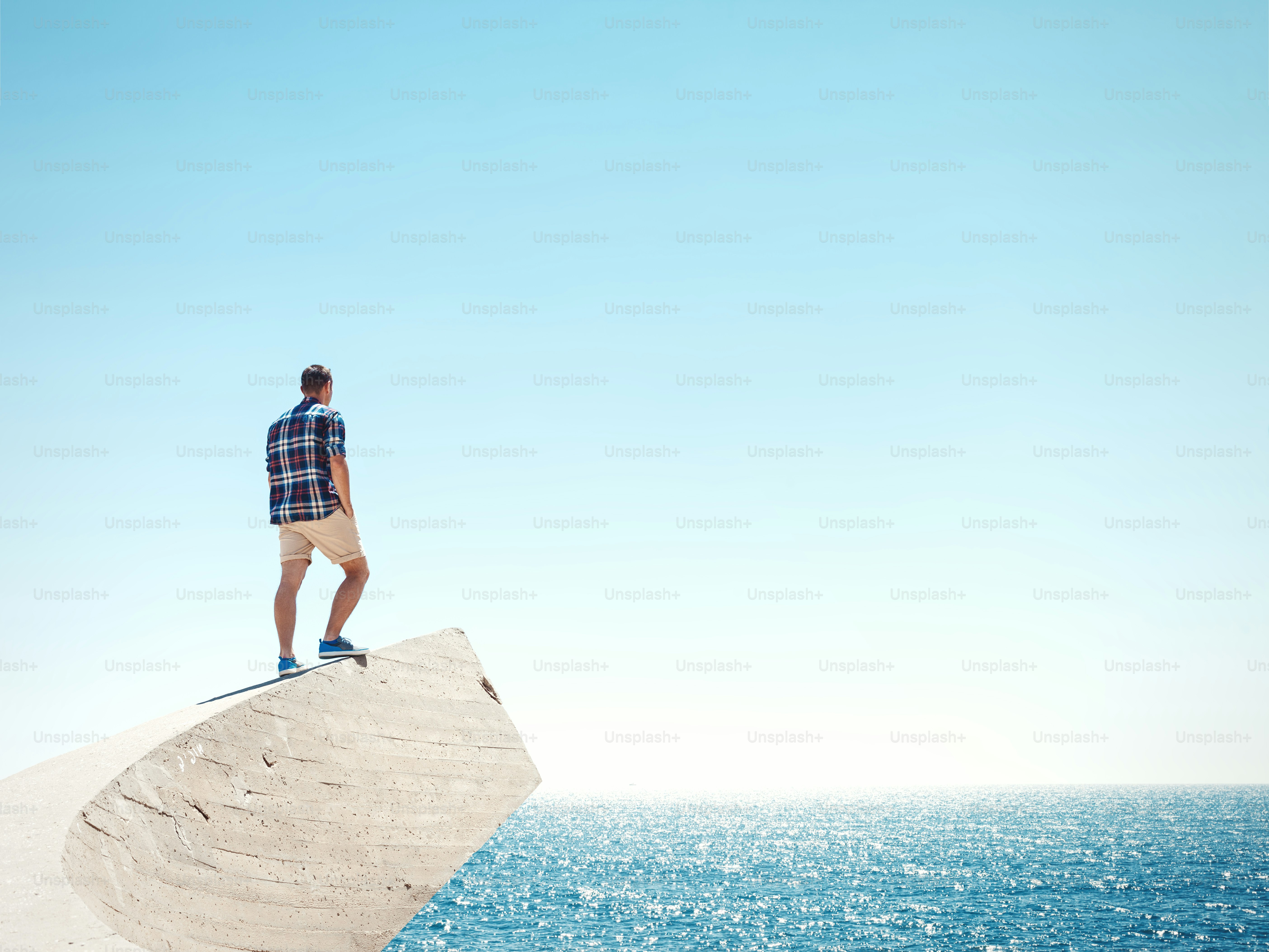 Young man standing on a peak and looking at the sea photo – Objectives ...