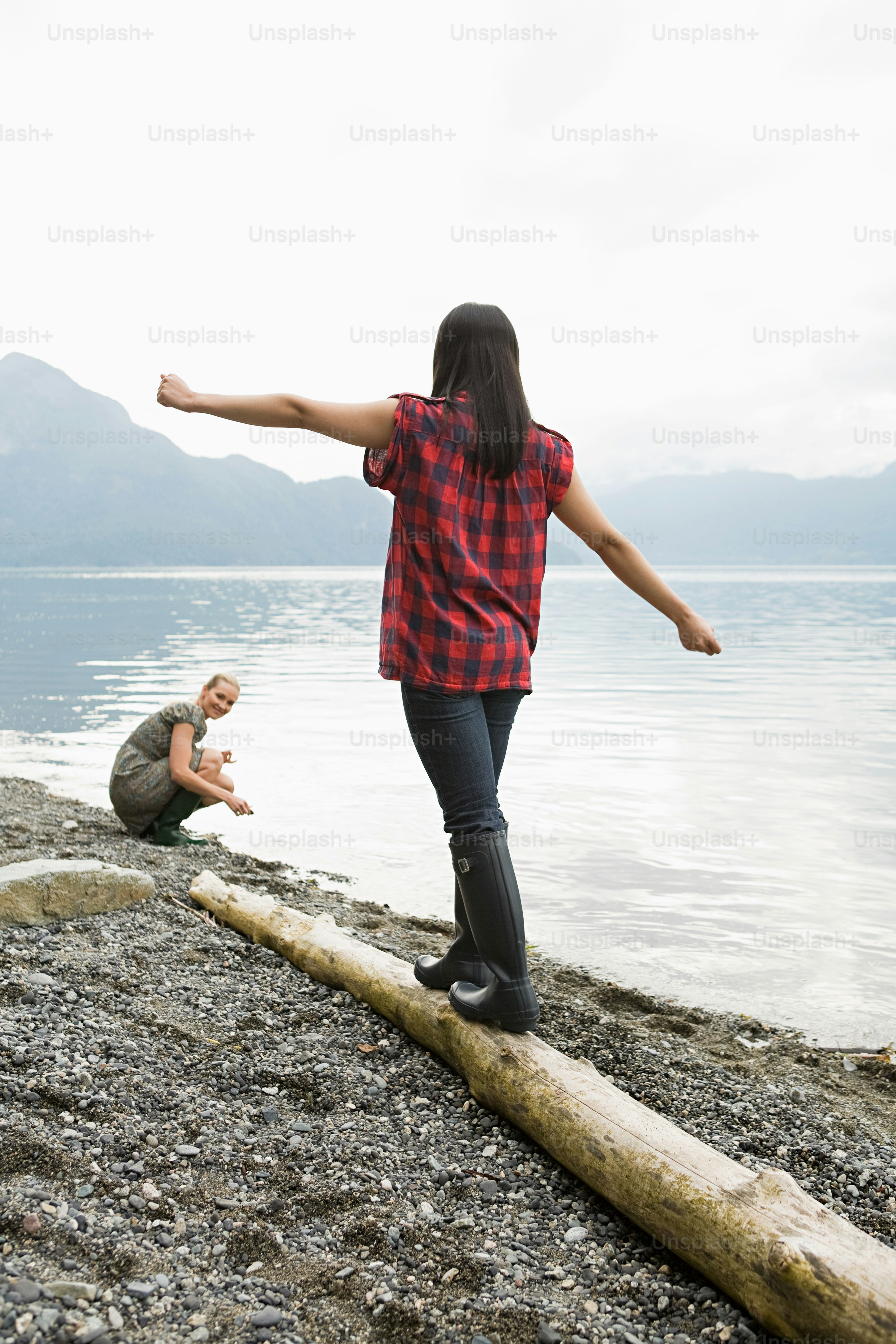A woman standing on top of a log next to a body of water photo ...