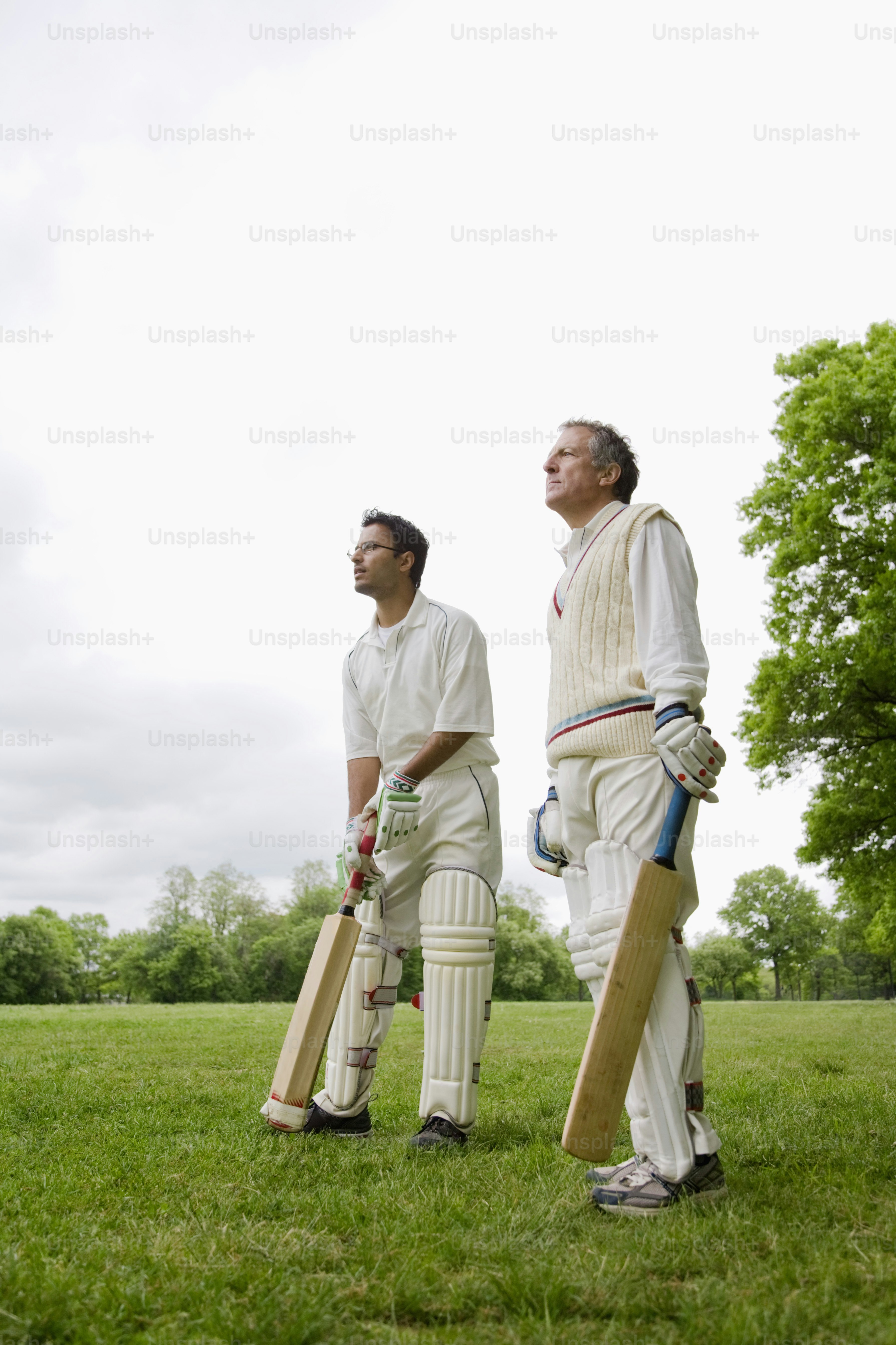 A couple of men standing on top of a lush green field photo – Cricket ...