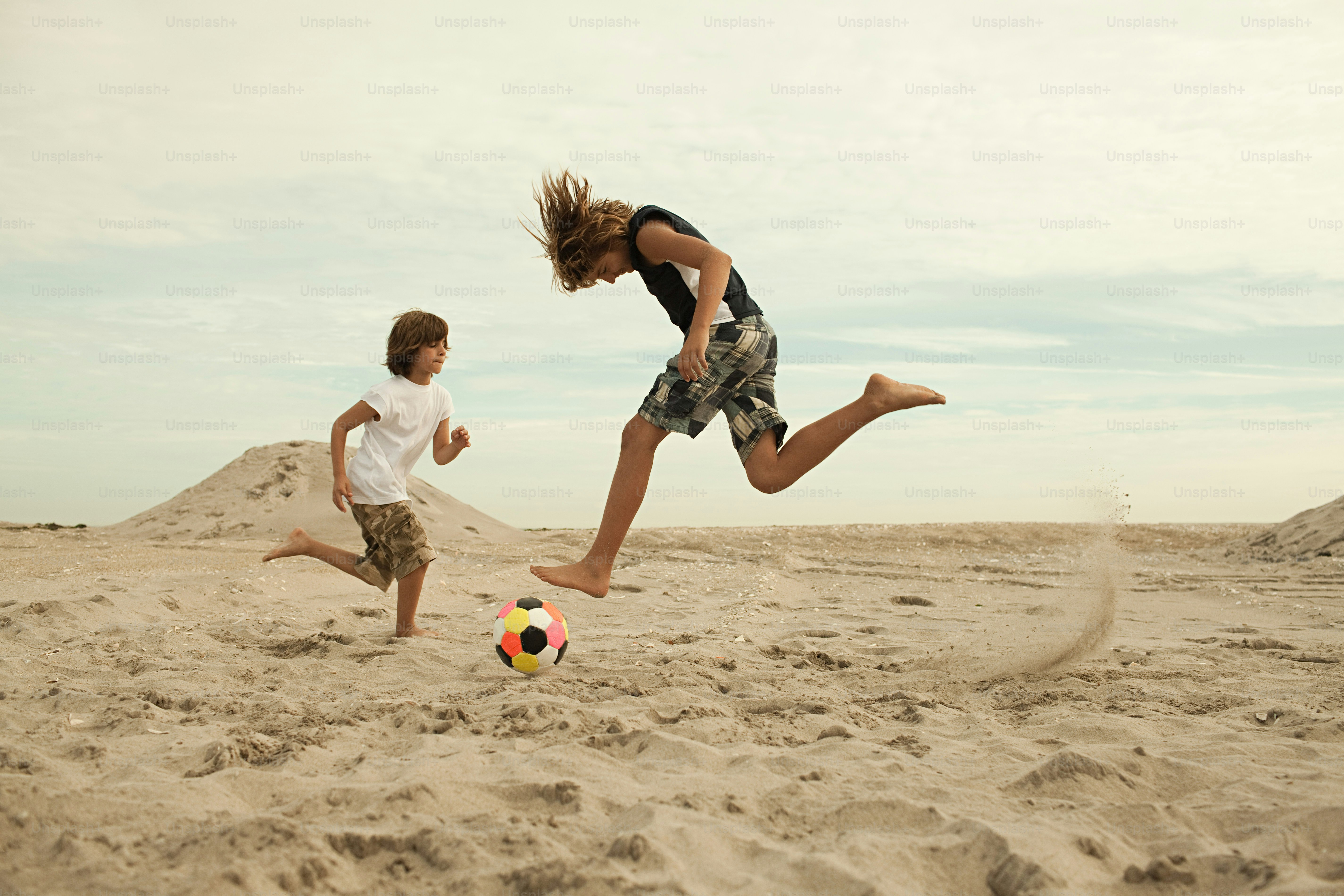 A boy and a girl playing soccer in the sand photo – Jumping Image on ...