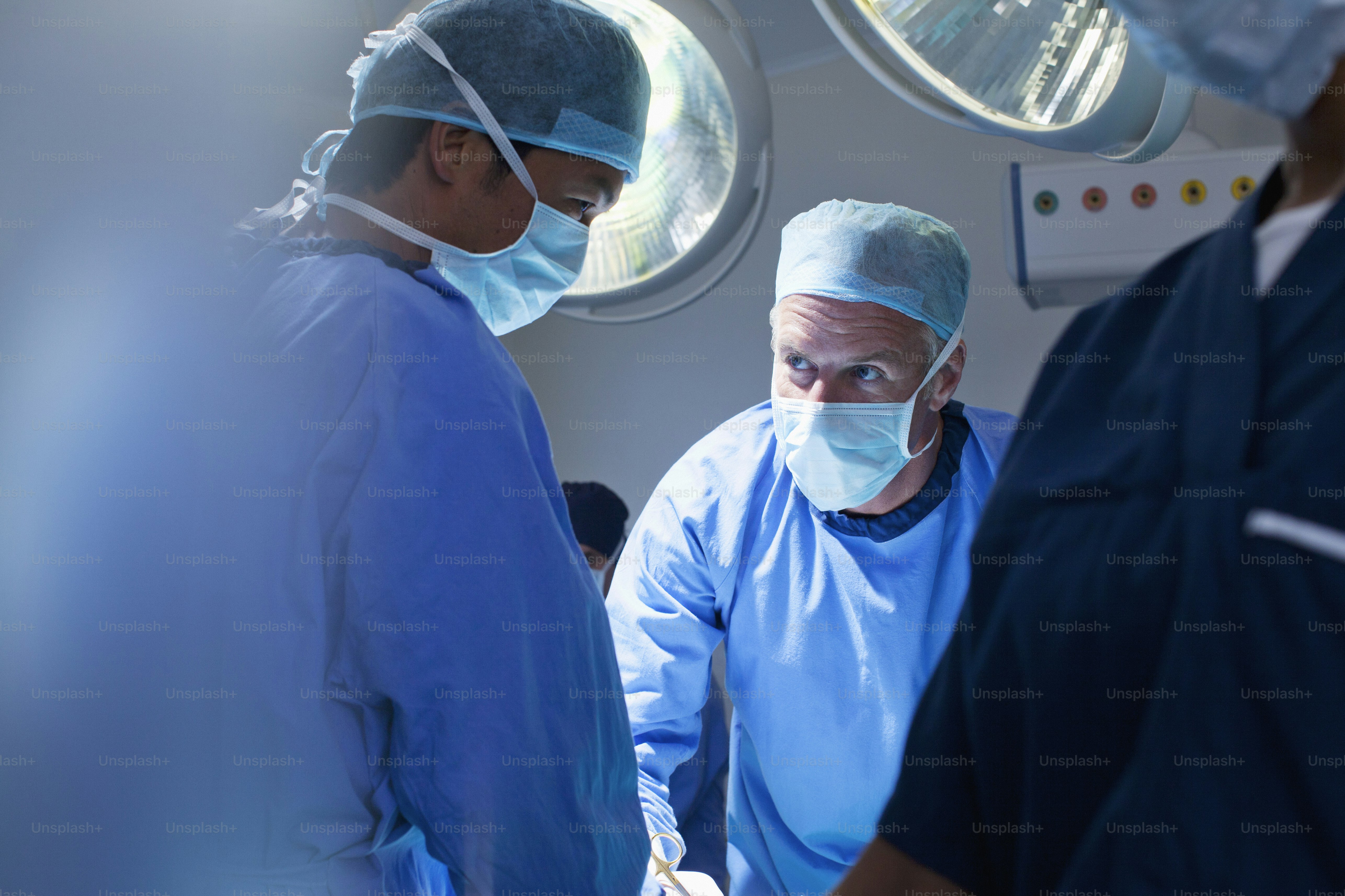 A group of doctors standing around each other photo – Surgical light ...