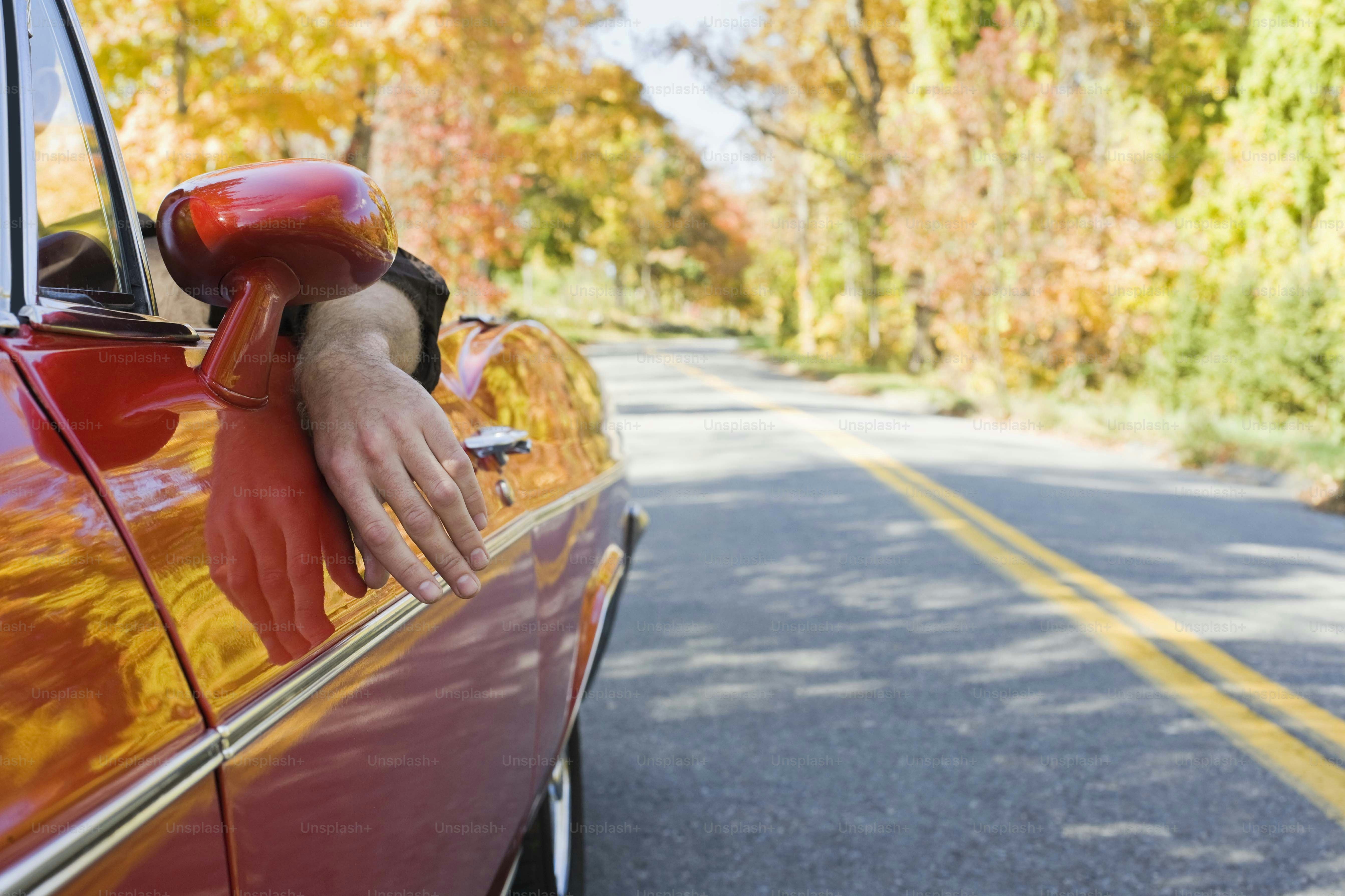 A person's hand sticking out of the window of a red car photo – Road ...