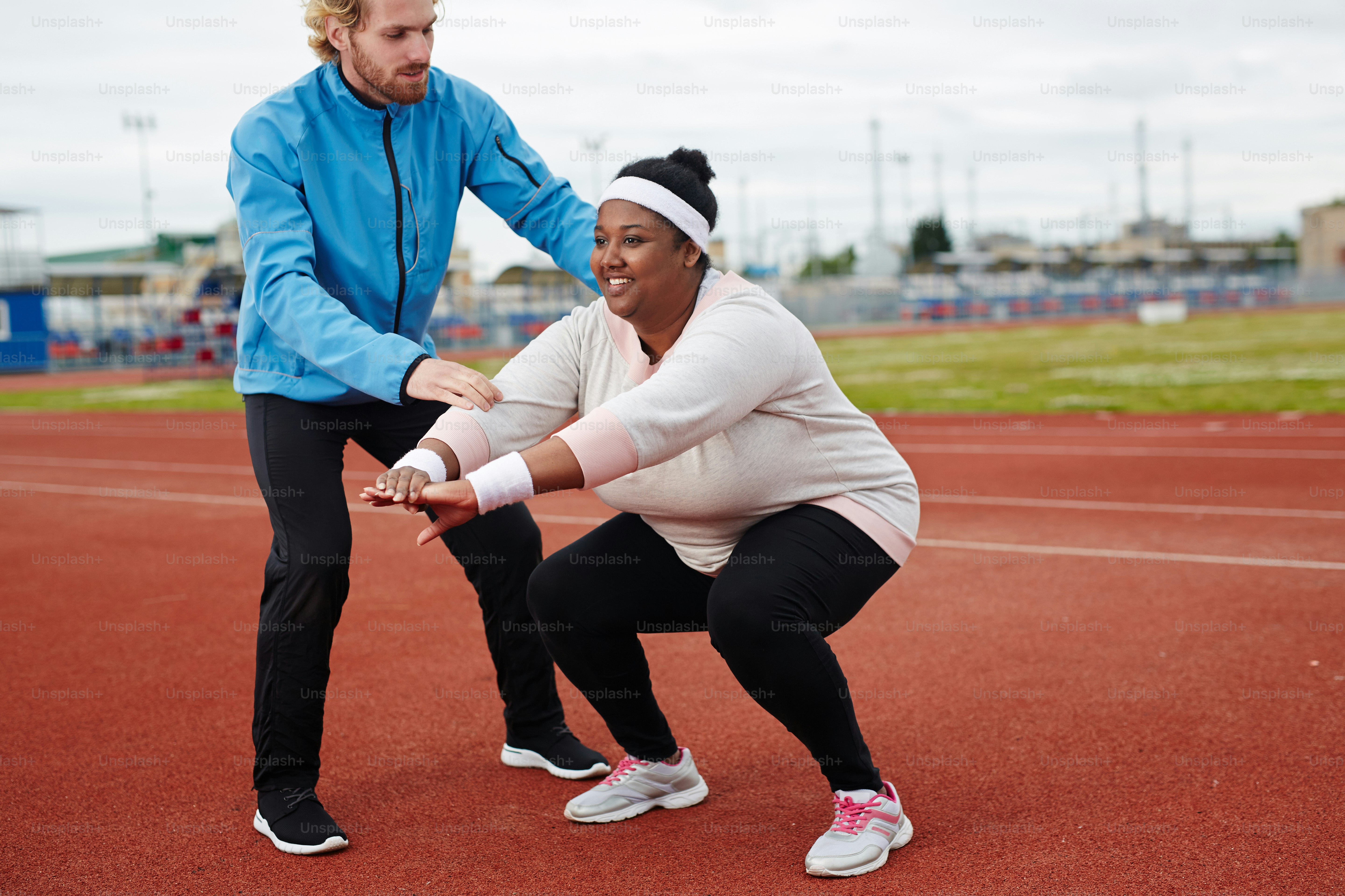 Happy young oversized female doing squat exercise with help of ...
