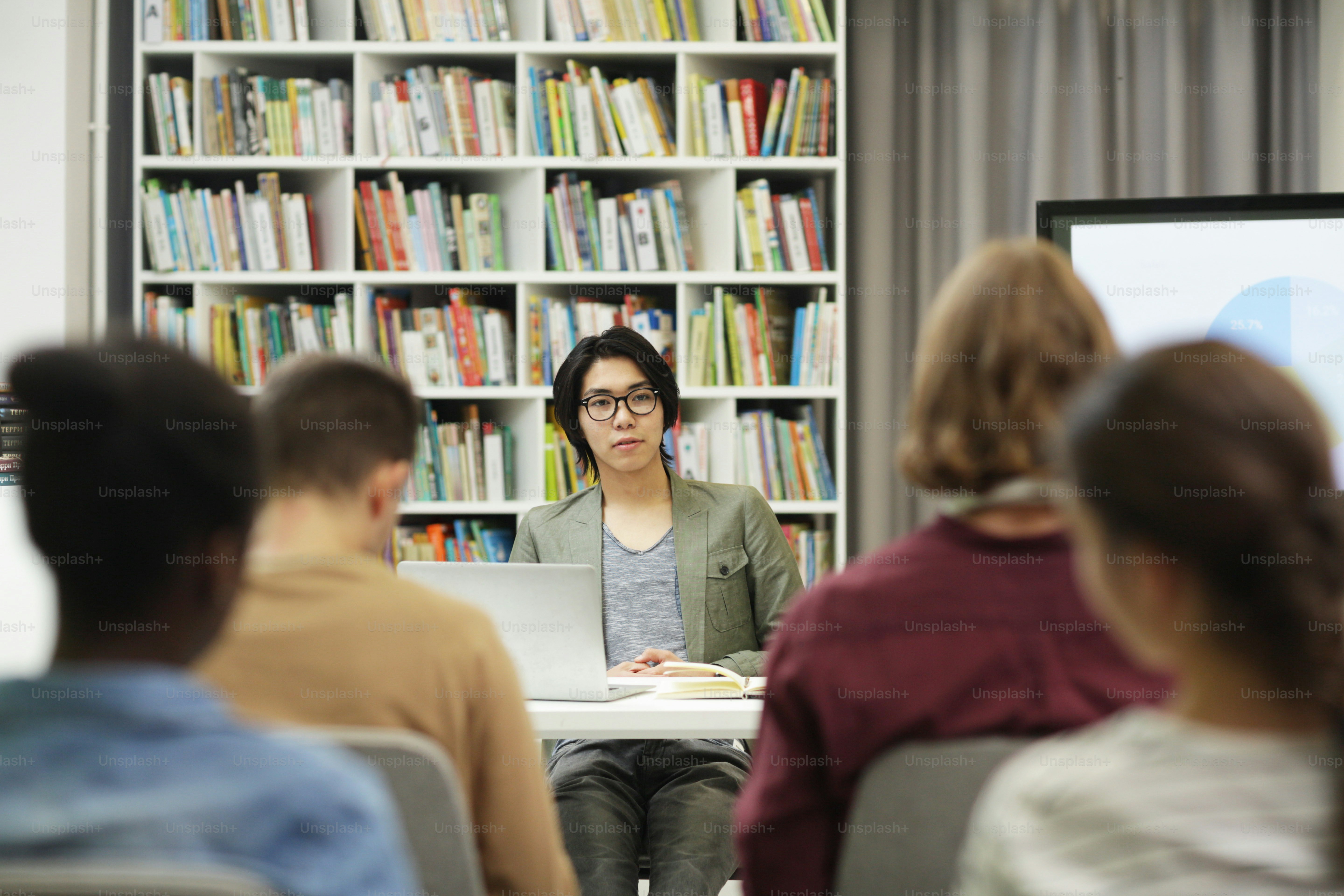 Young Asian writer sitting at the table and presenting his new book to ...